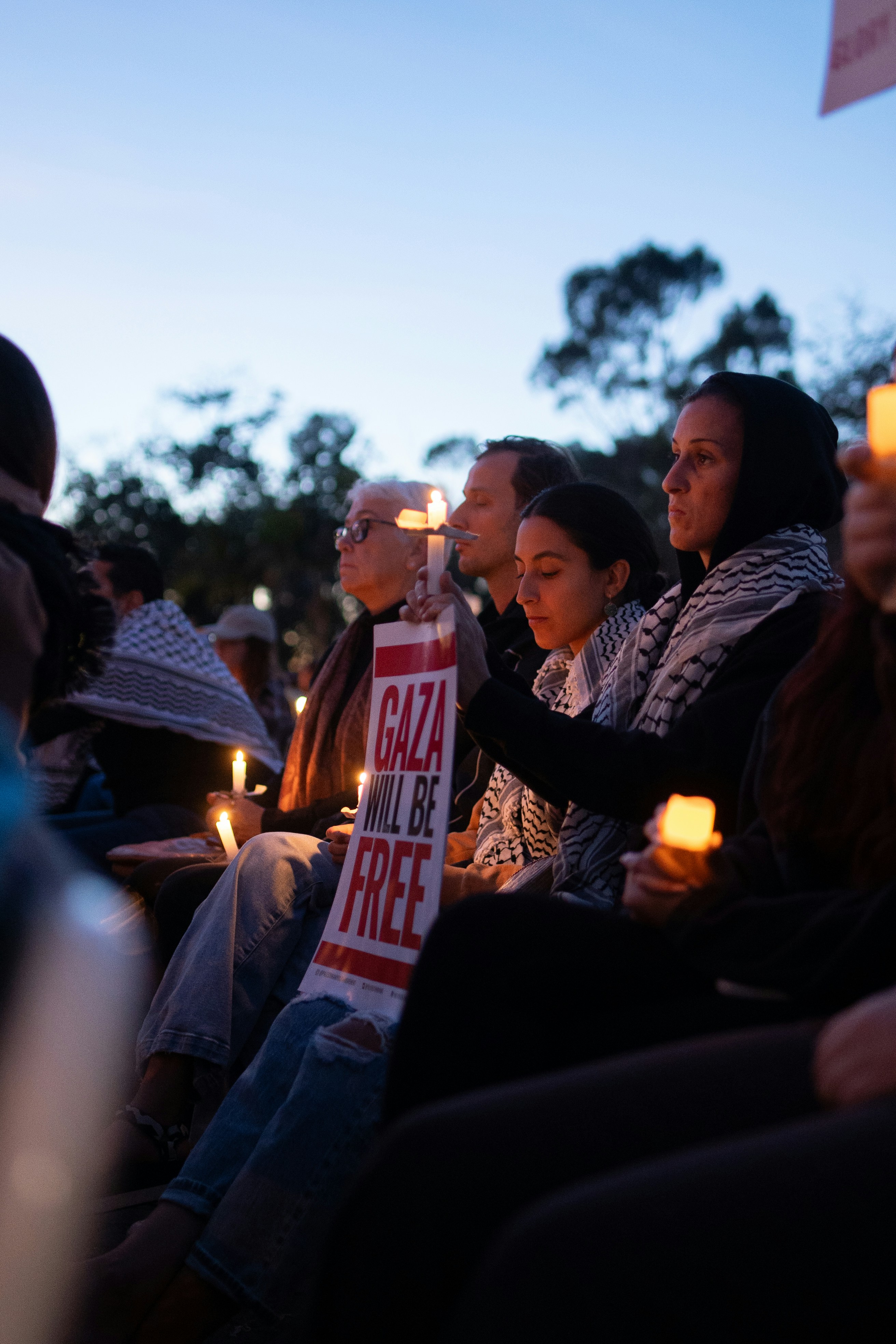 Candlelit vigil: faces and signs in a dusk crowd