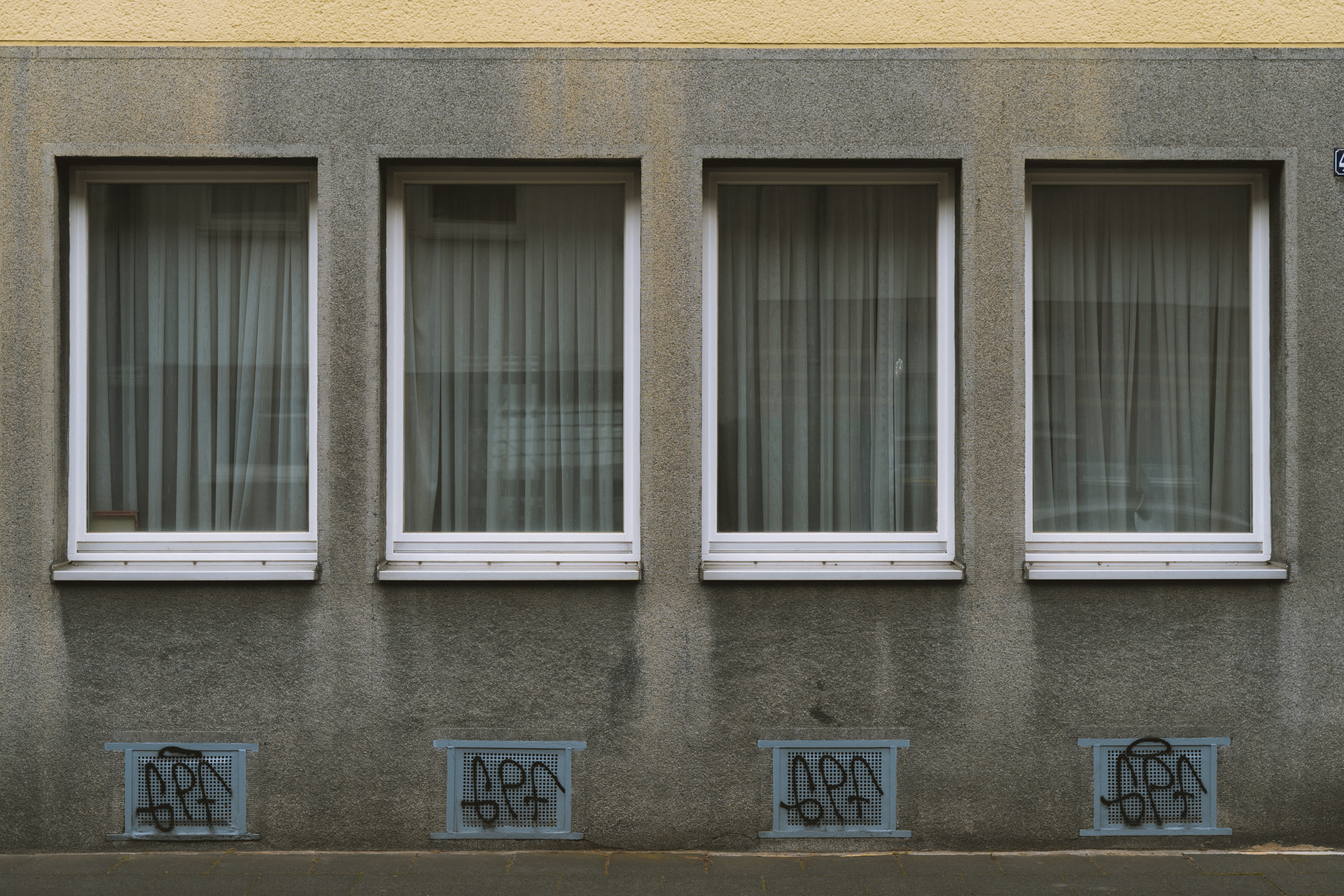 Quiet Facade: Four Window Panels and a Graffiti Vent Row