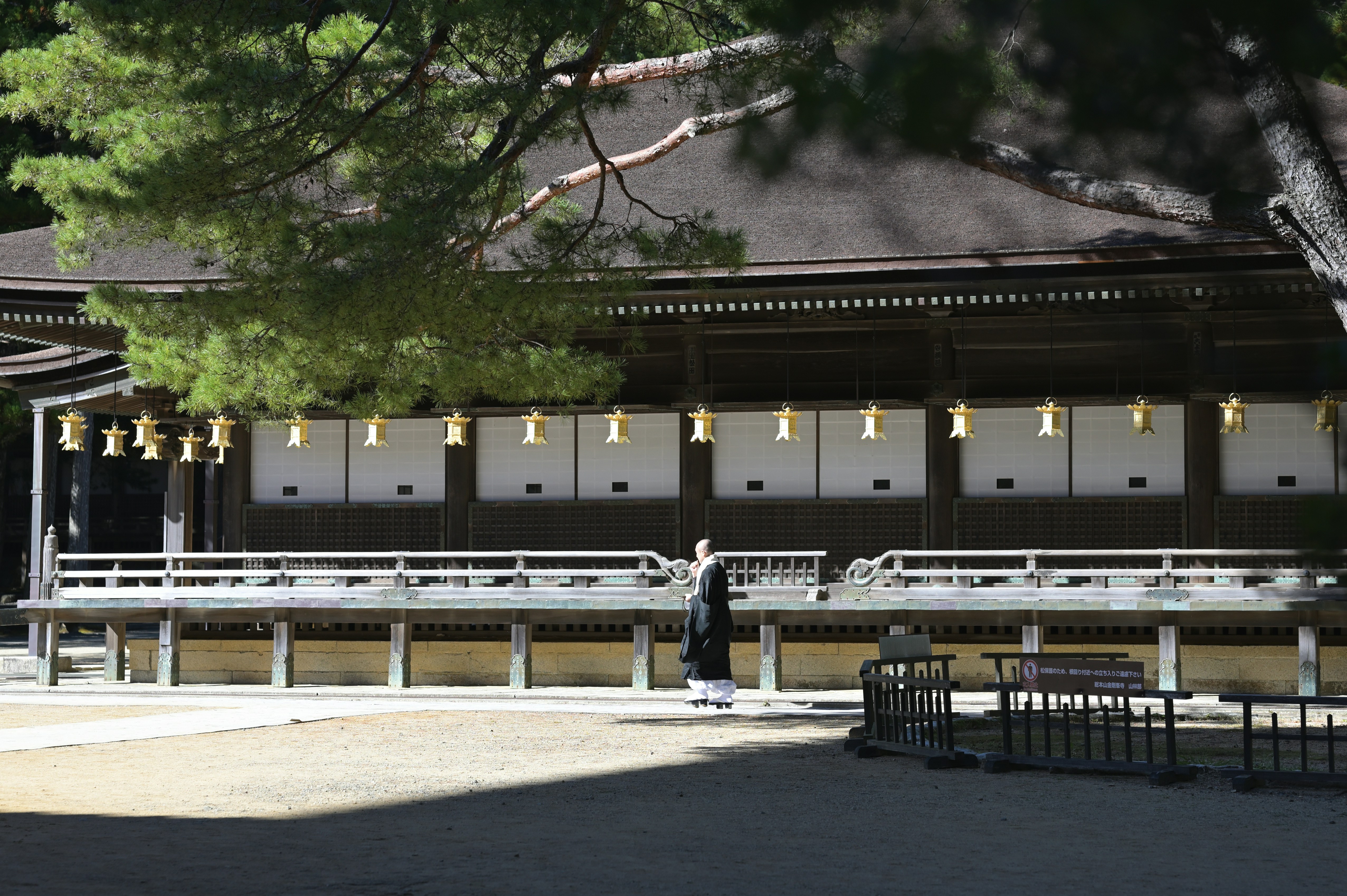 Lone pilgrim threads the wooden veranda beneath lanterns at a tranquil Shinto temple