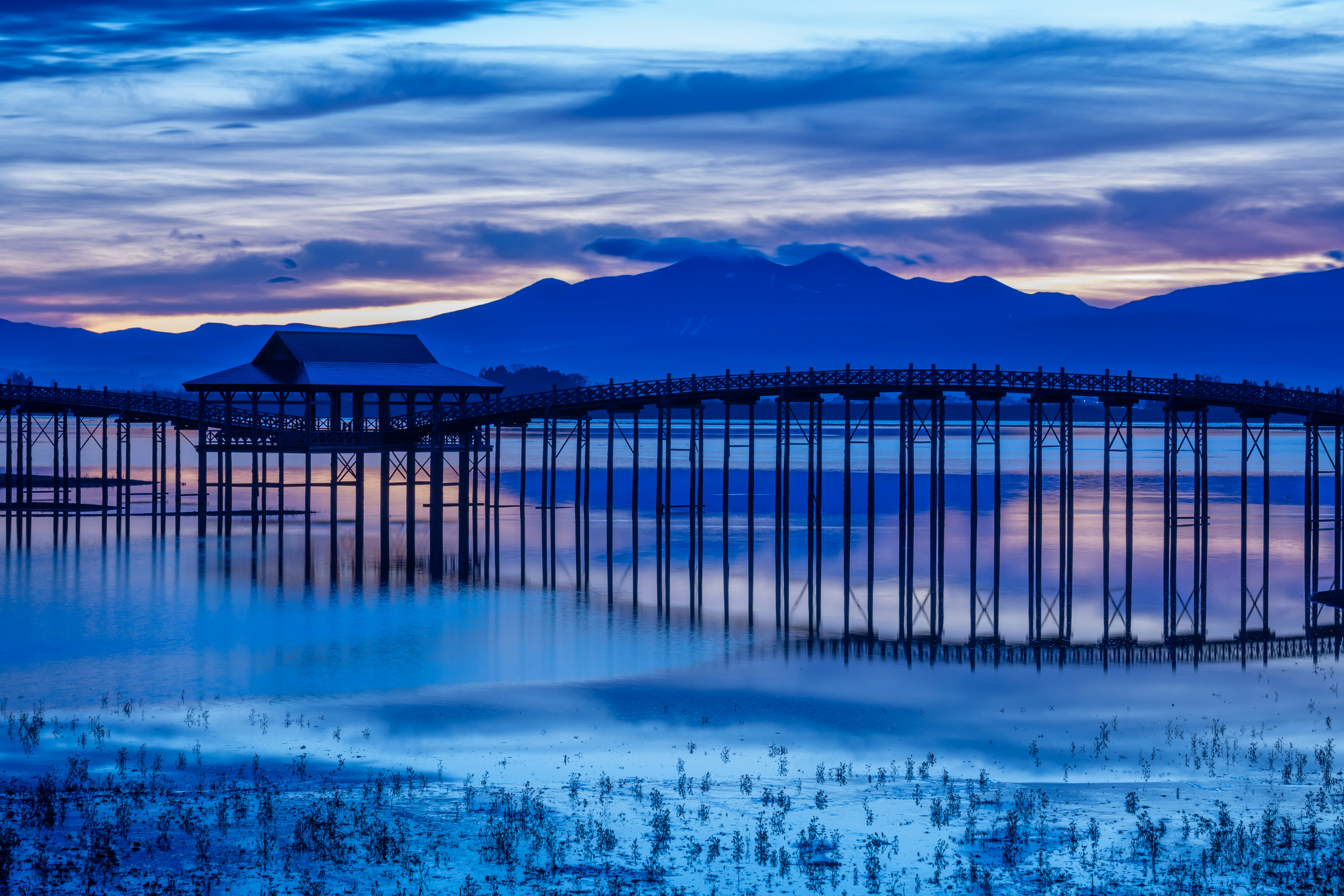 A bridge over a body of water with mountains in the background photo ...