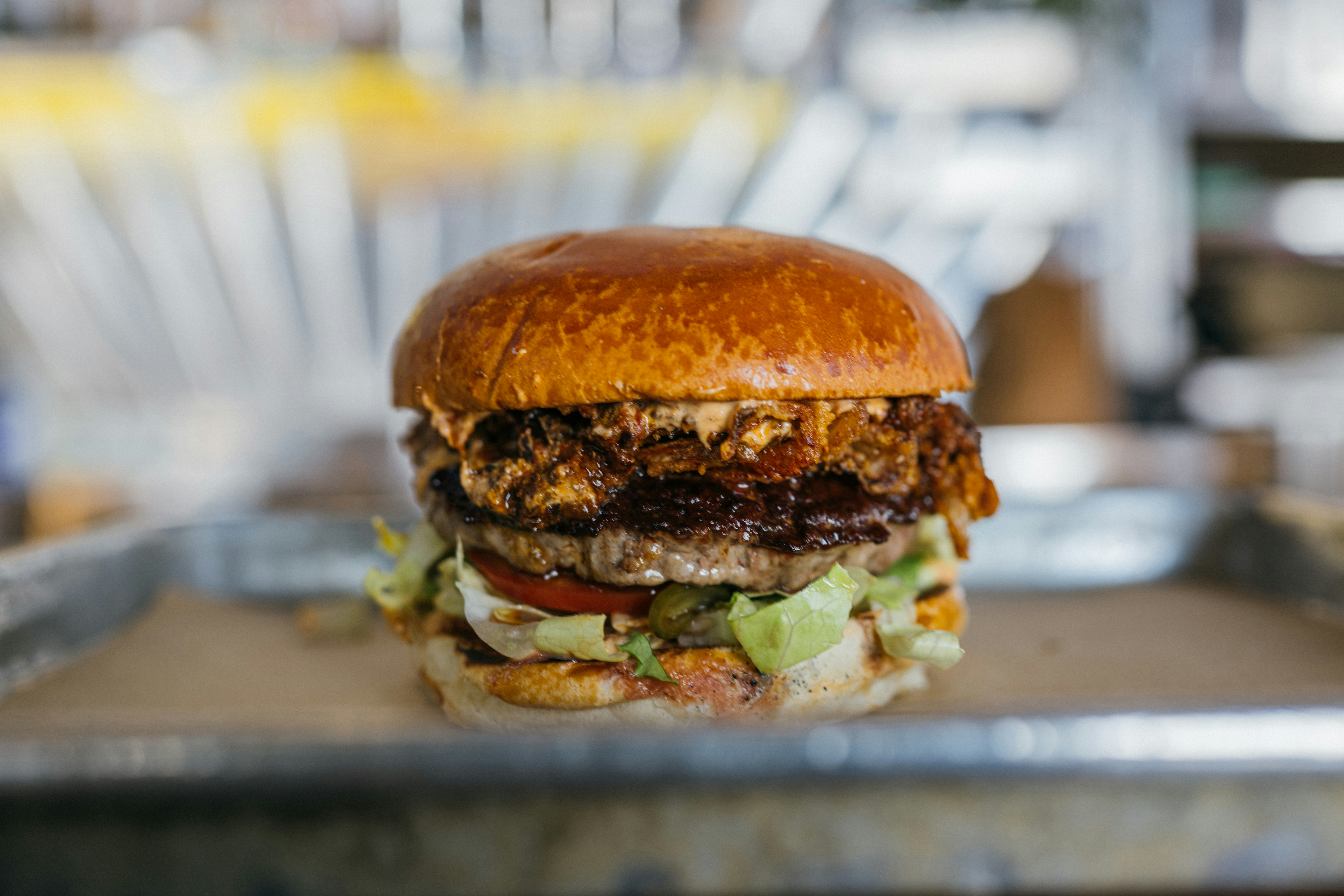 Juicy burger stacked with layers of lettuce, tomato, and crispy onions on a metal tray.