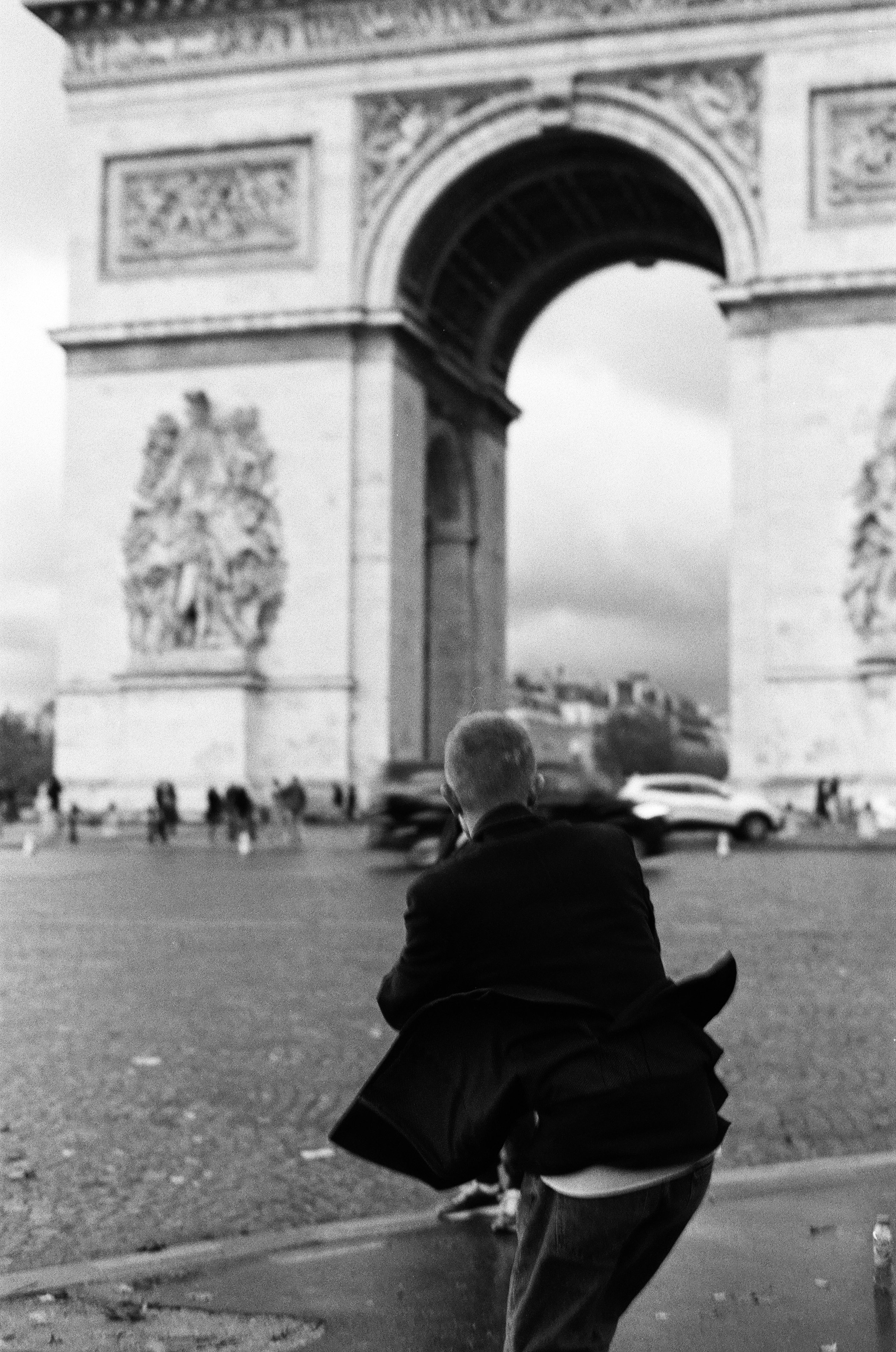 A black and white photo of a man running in front of the arc de trio ...