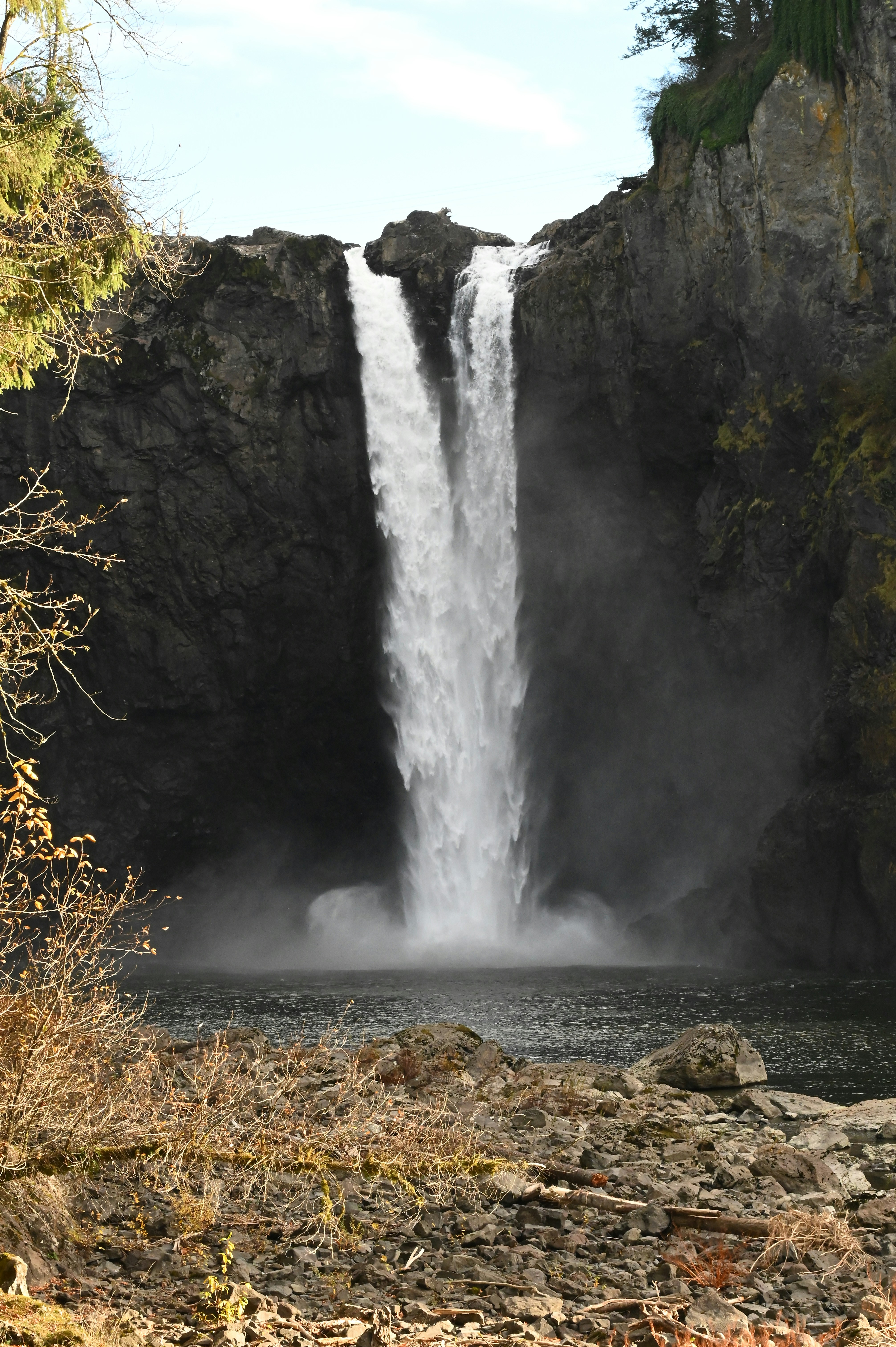 Majestic waterfall cascading down rocky cliffs, surrounded by lush greenery and mist rising from the water's surface.