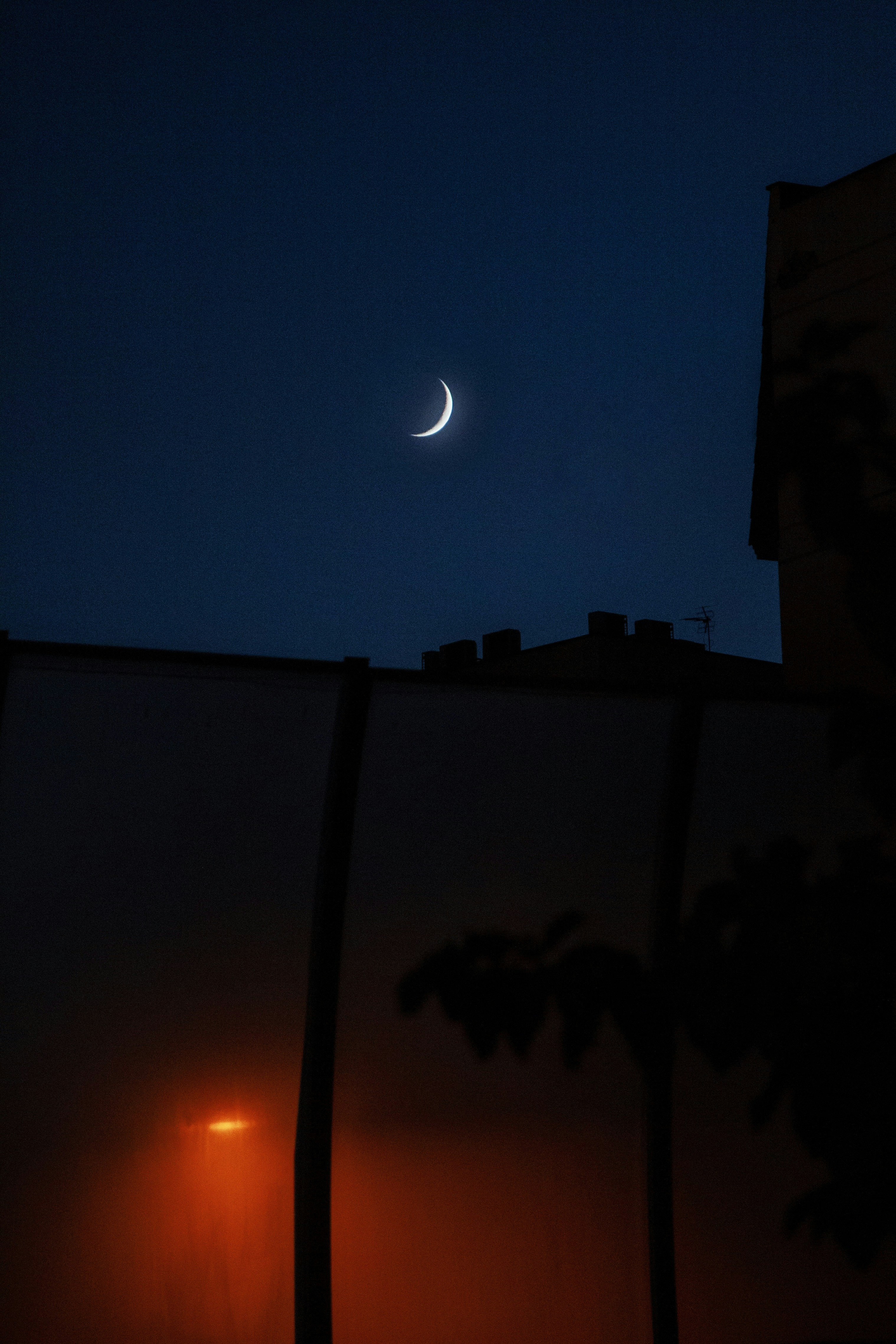 Moon Crescent Over Rooftops and Warm Streetlight Glow
