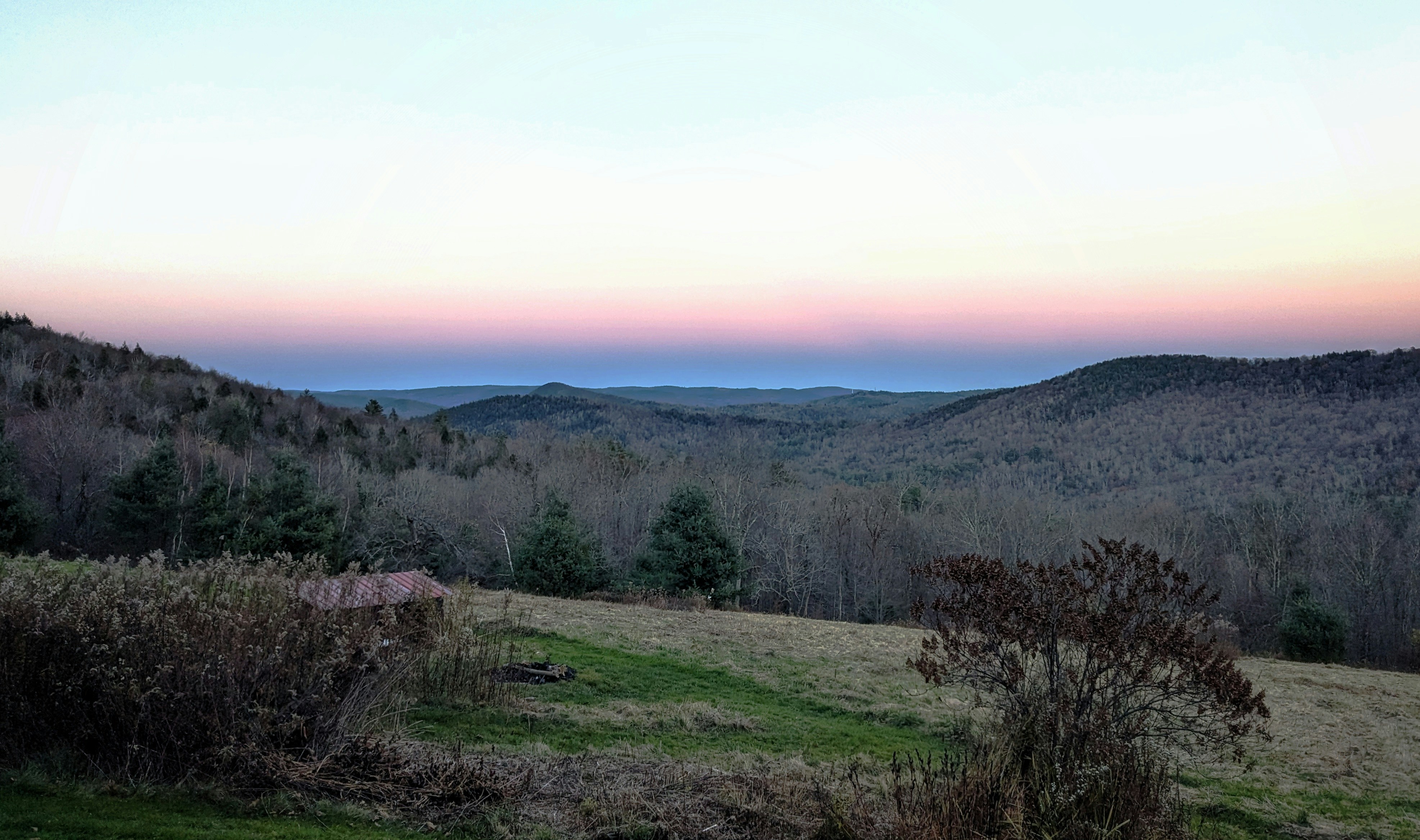 Pastel sky over rolling hills and a grassy foreground at dusk.