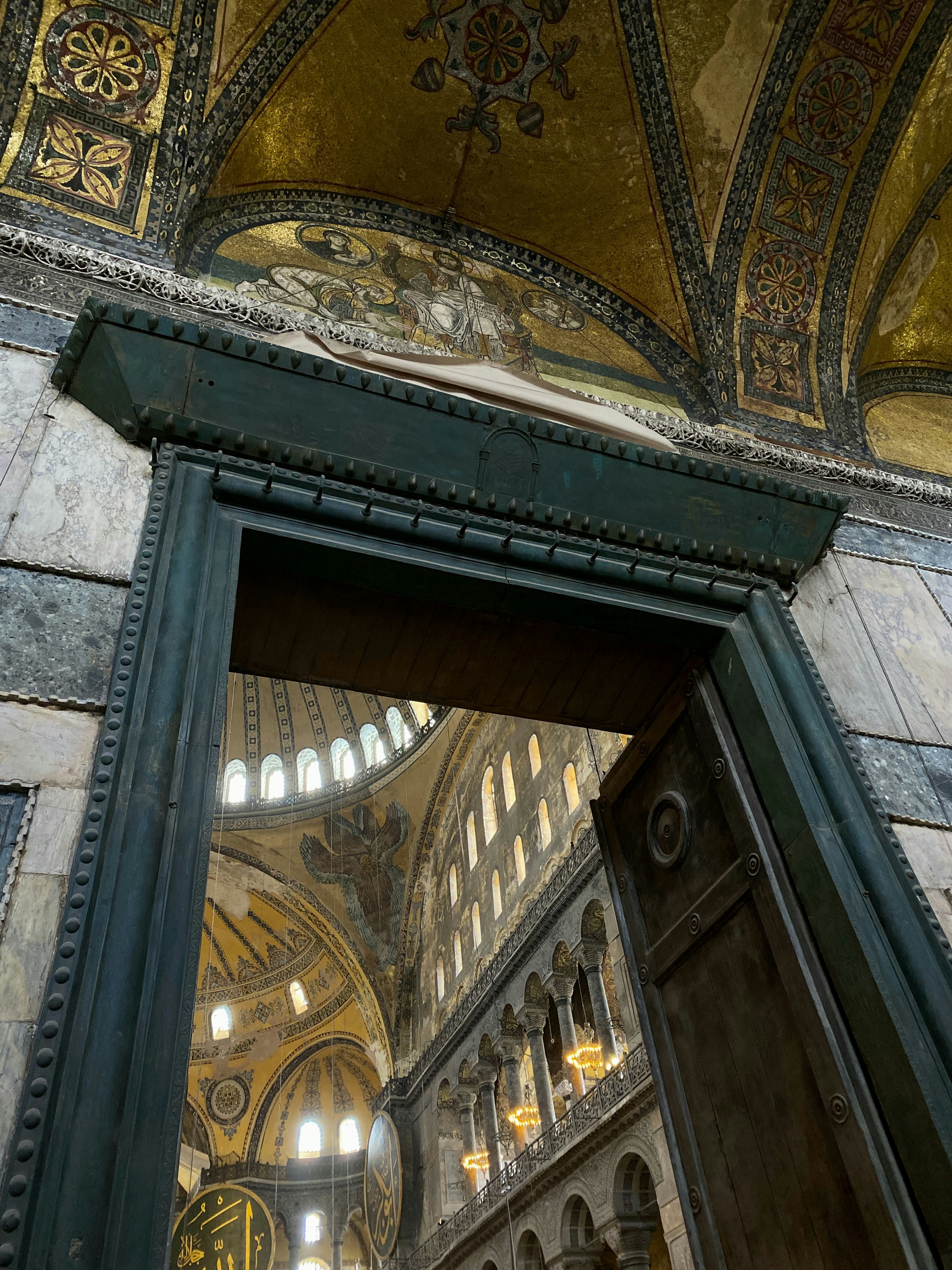 Ornate interior of Hagia Sophia viewed through an open door, showcasing intricate mosaics and soaring arches.