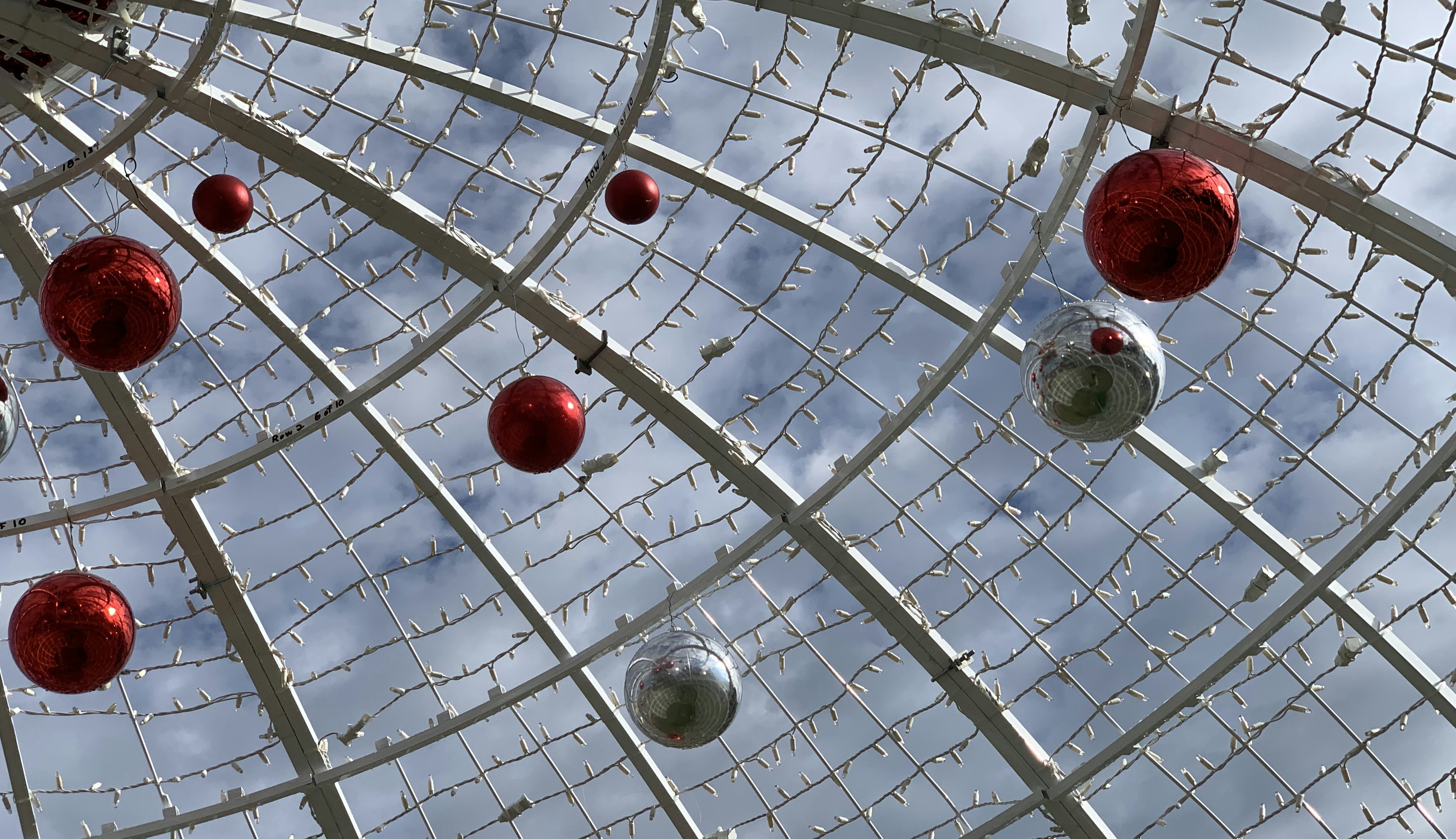 A whimsical display of red and silver ornaments hanging from a lattice structure, set against a backdrop of a cloudy sky.