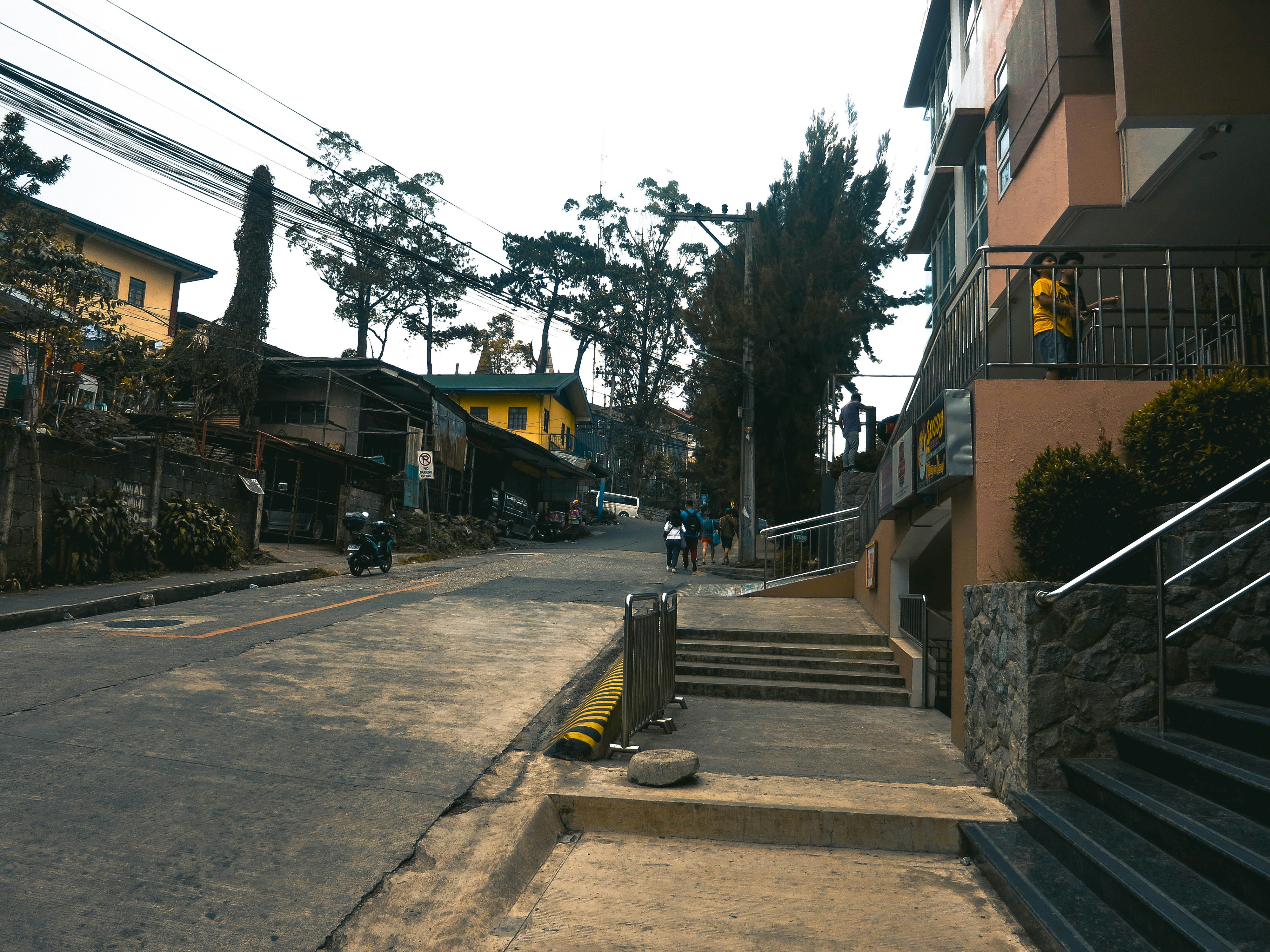 City street with upward stairs flanked by buildings and trees under a bright sky.