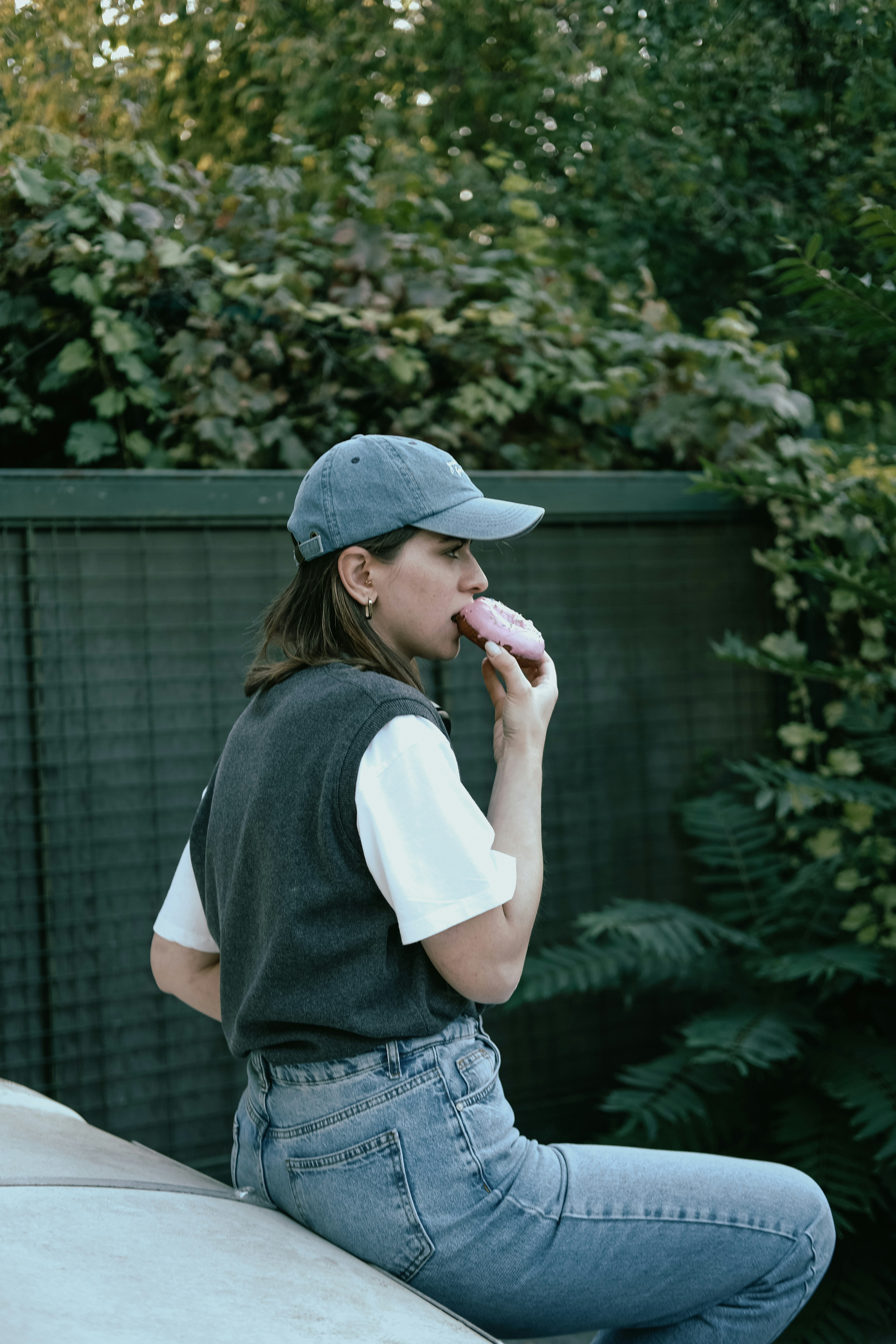 A woman sitting on a ledge eating a donut photo – Free Person Image on ...