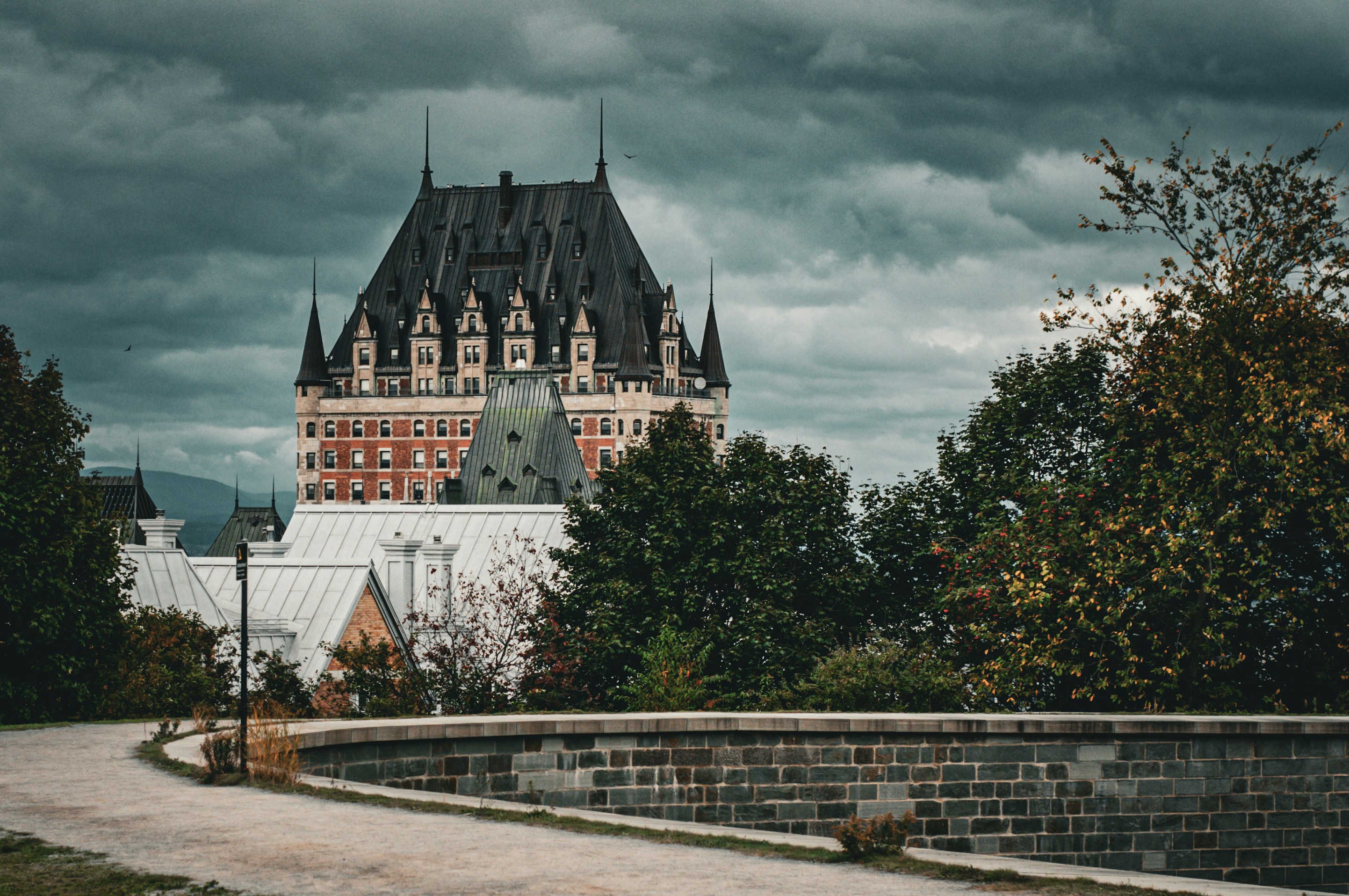Castle silhouette under a brooding sky framed by autumn trees along a stone promenade