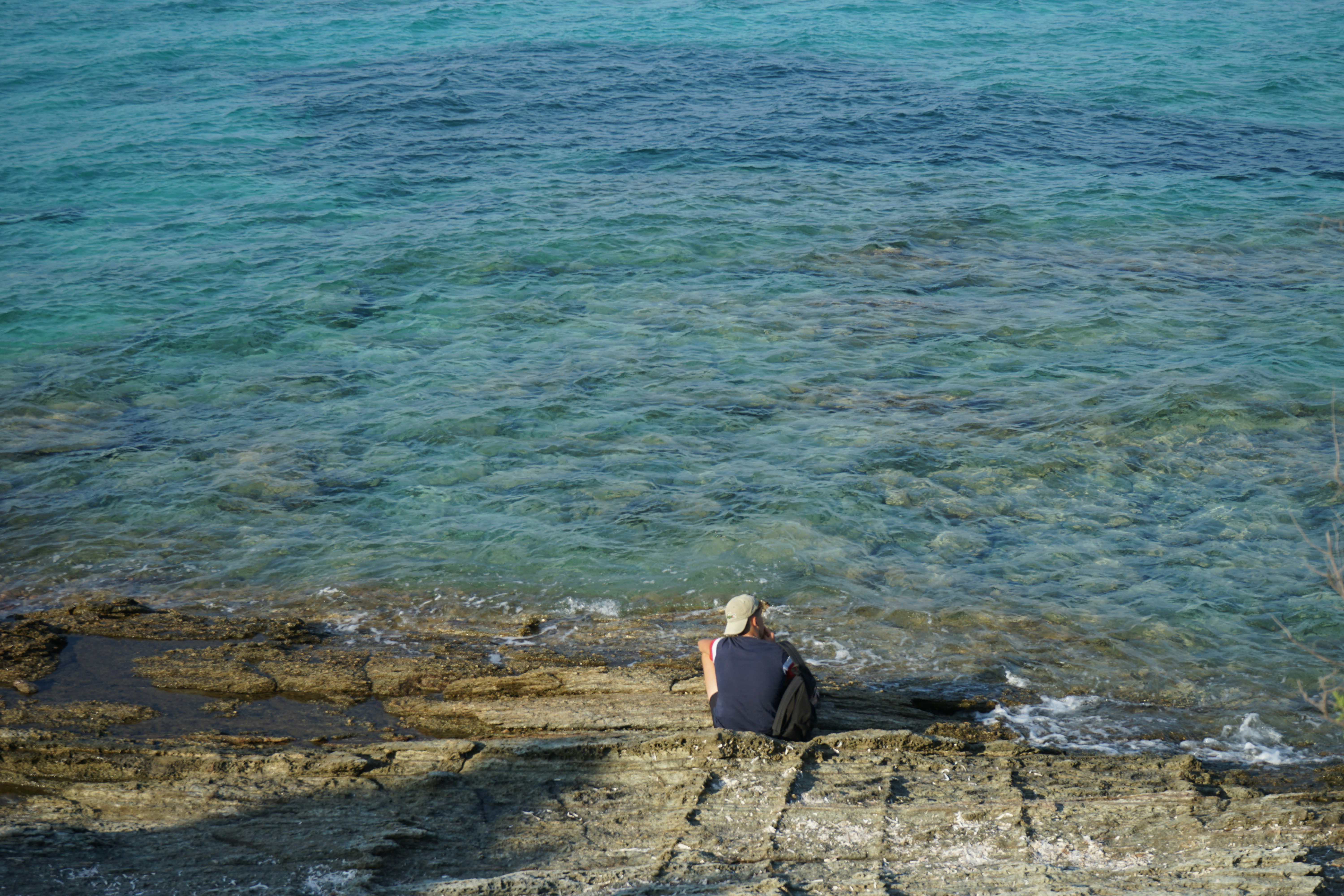 Homme assis sur les rochers face à la mer