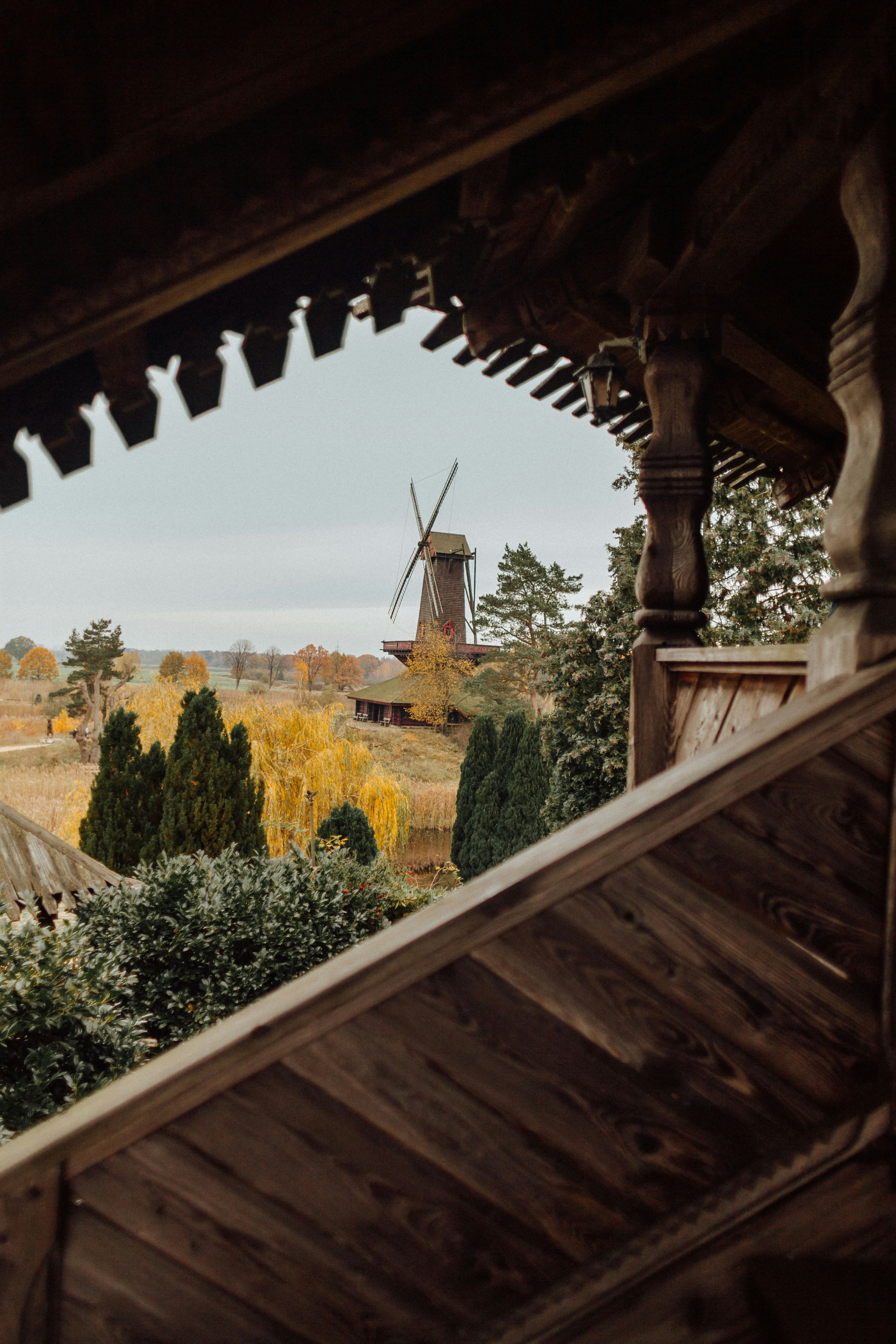 Autumn Windmill Framed by Carved Timber and a Shadowed Balcony