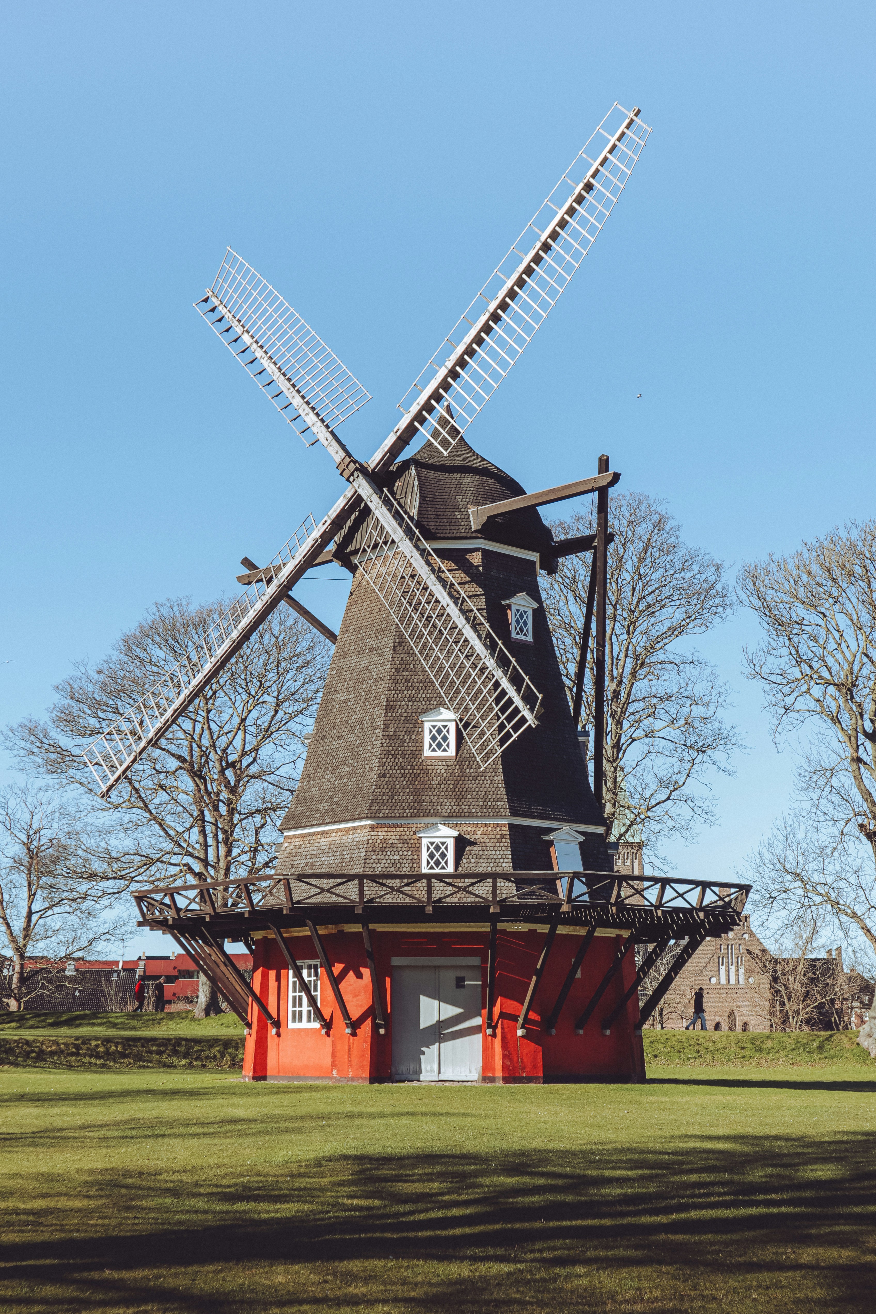 Traditional windmill standing proudly against a clear blue sky, surrounded by lush greenery. The structure showcases intricate design and craftsmanship.