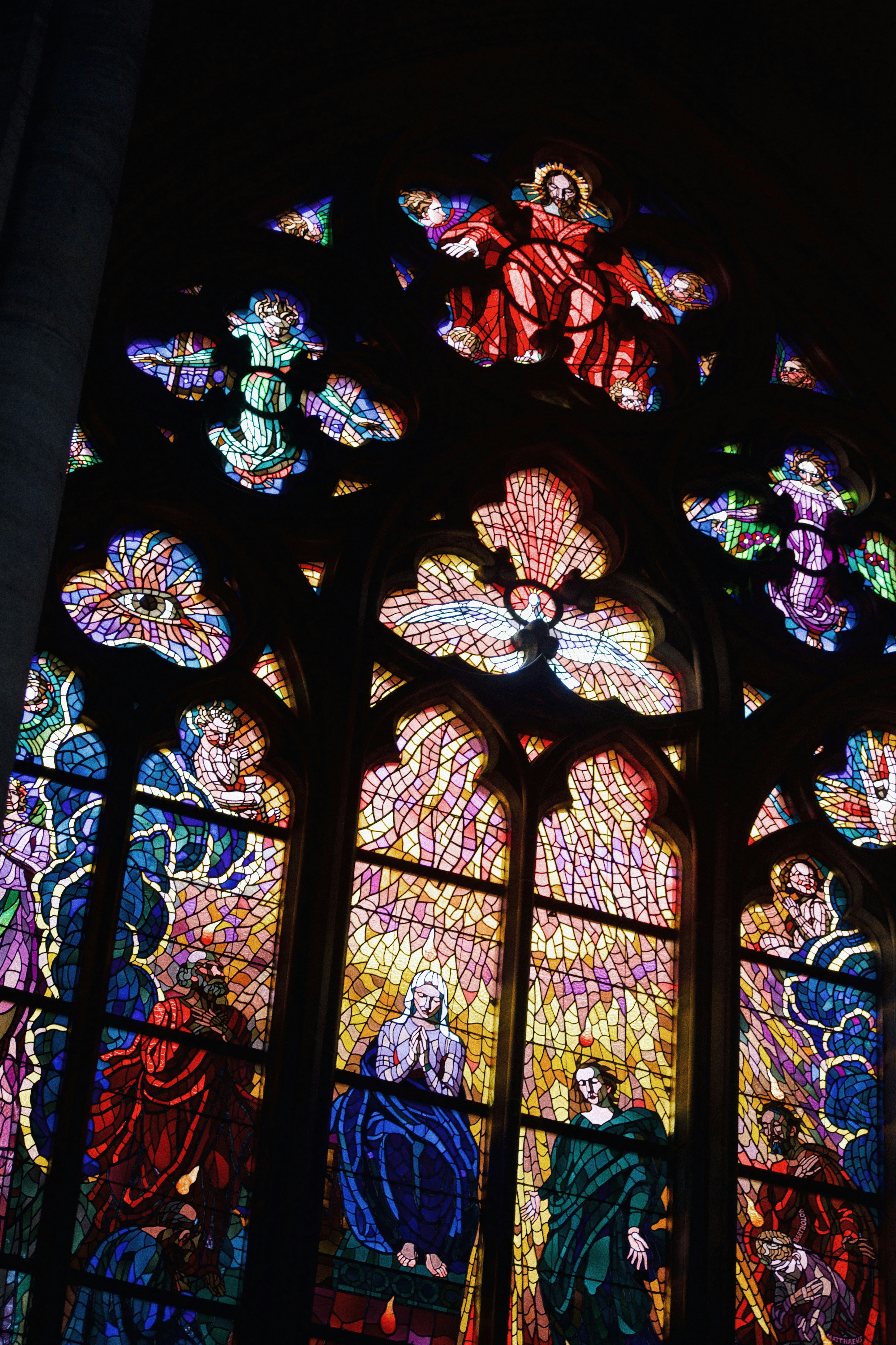 Intricate stained glass window depicting biblical figures and celestial scenes, illuminated by natural light.