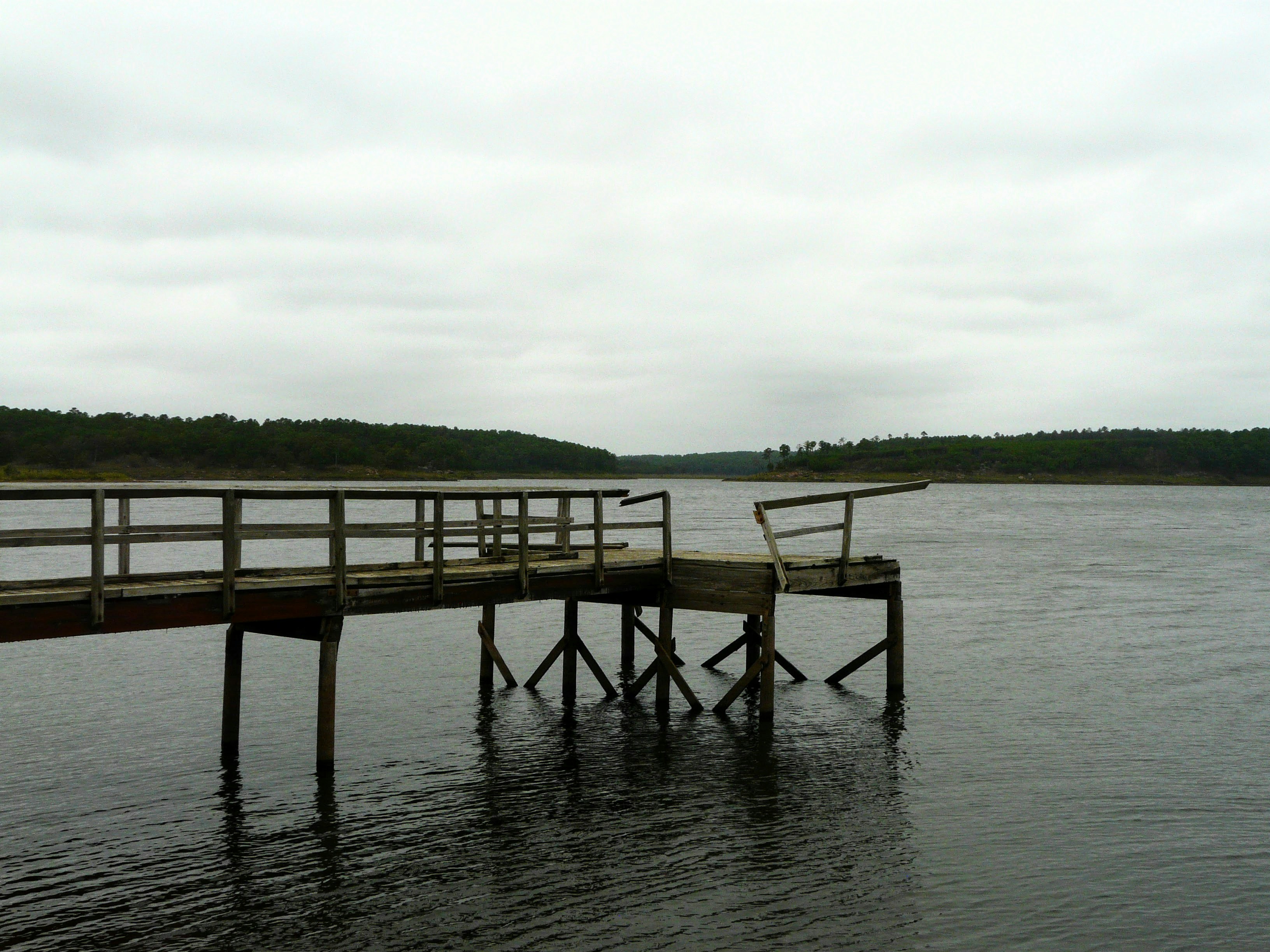 Weathered wooden dock extending into a tranquil lake under a cloudy sky.