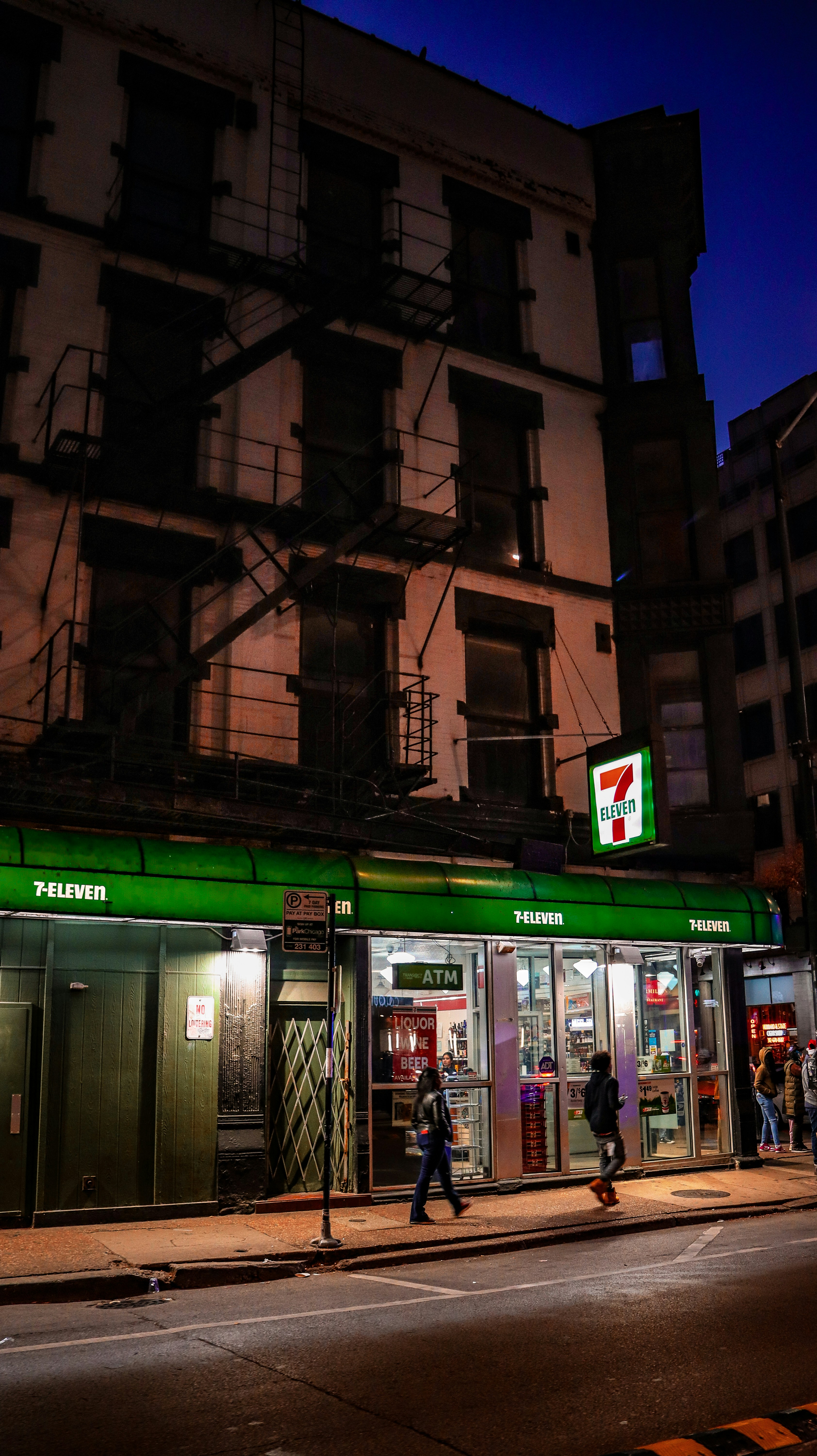 Neon Pulse on a Night Corner: 7-Eleven Beneath Fire Escapes