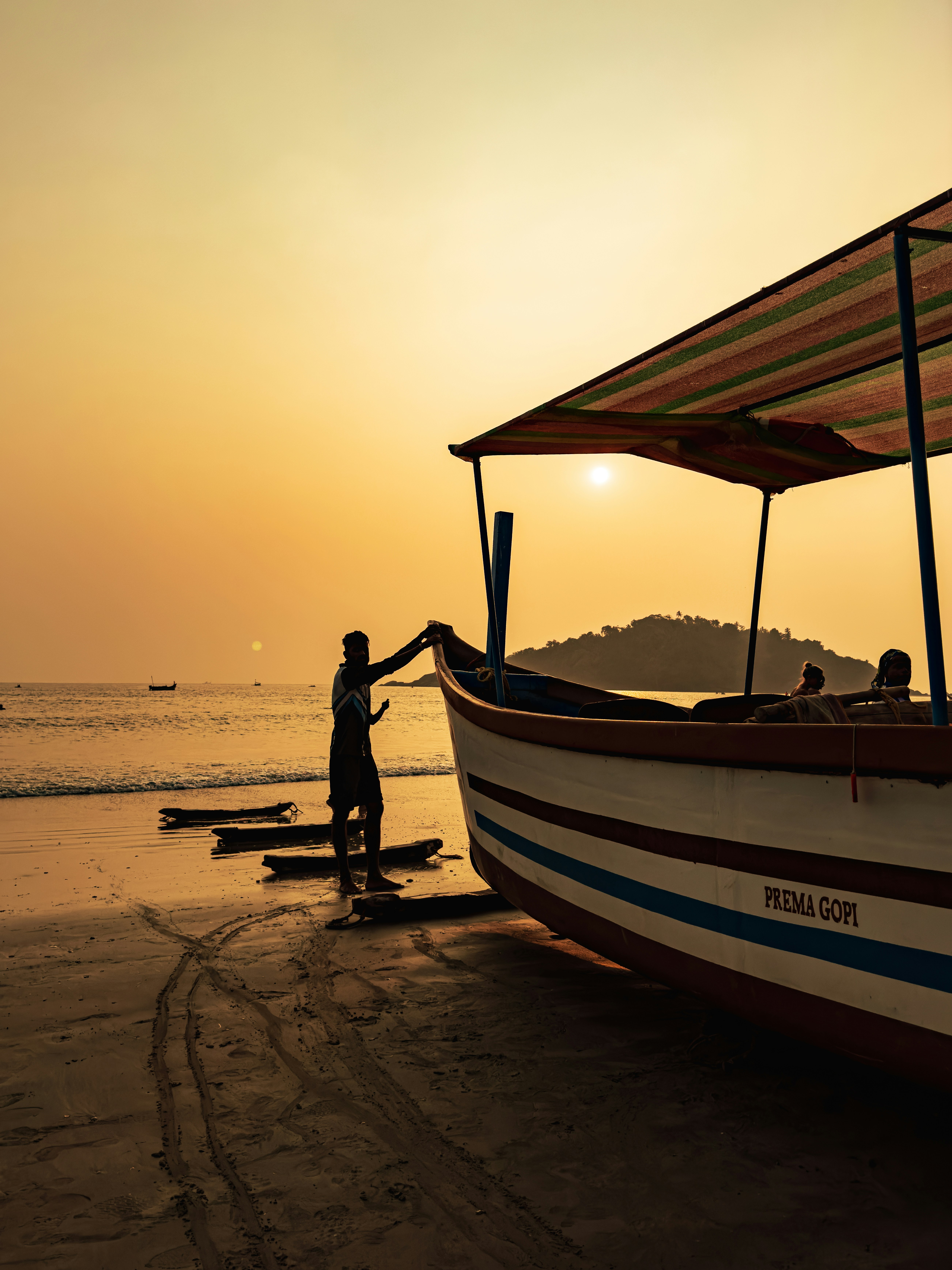 Fisherman preparing a boat on the beach at sunset, with silhouettes against a vibrant orange sky. The scene captures the tranquility of coastal life.