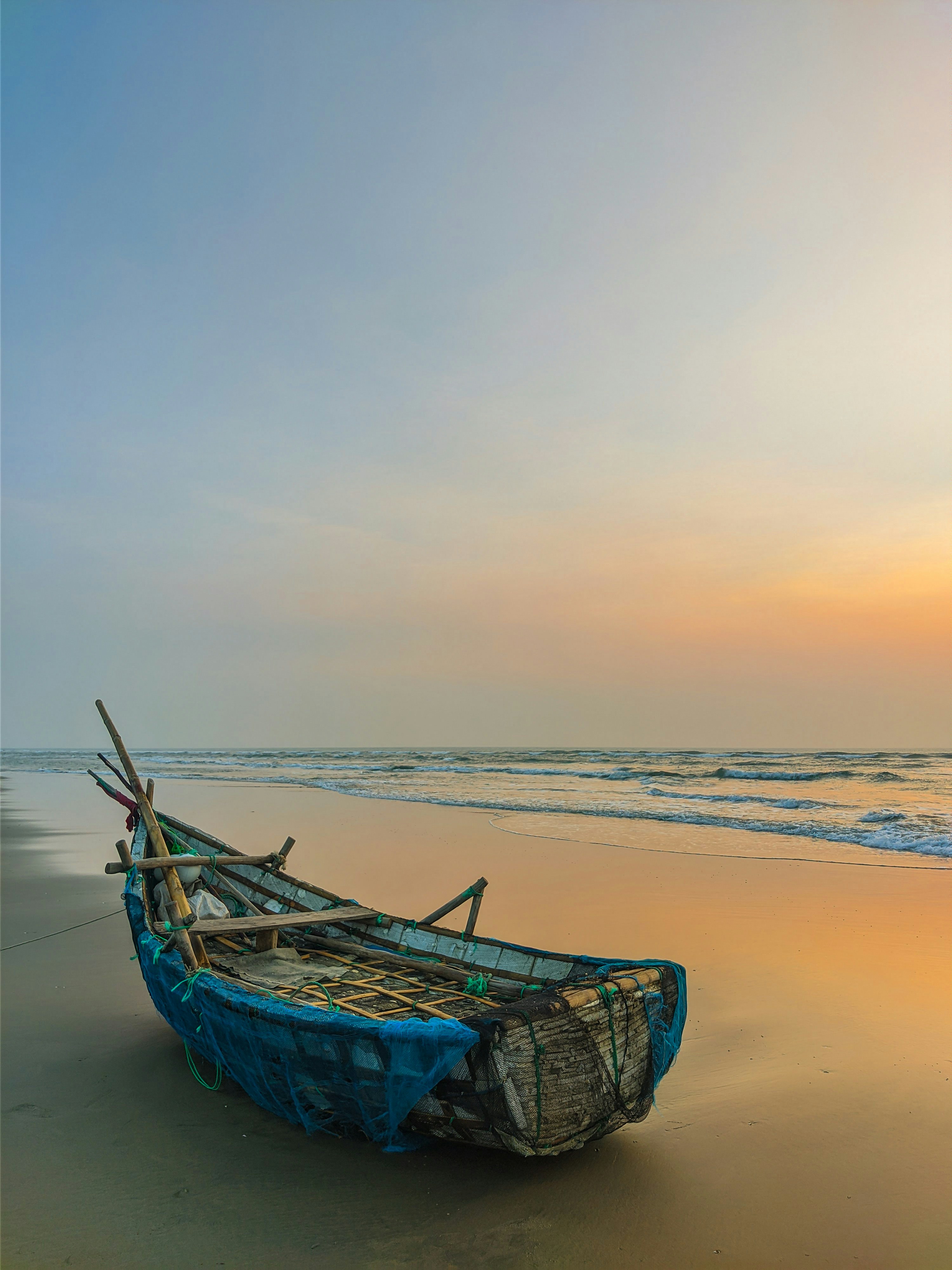 Weathered blue boat rests on the wet sand as a calm sea glows under a sunset sky in this photograph.