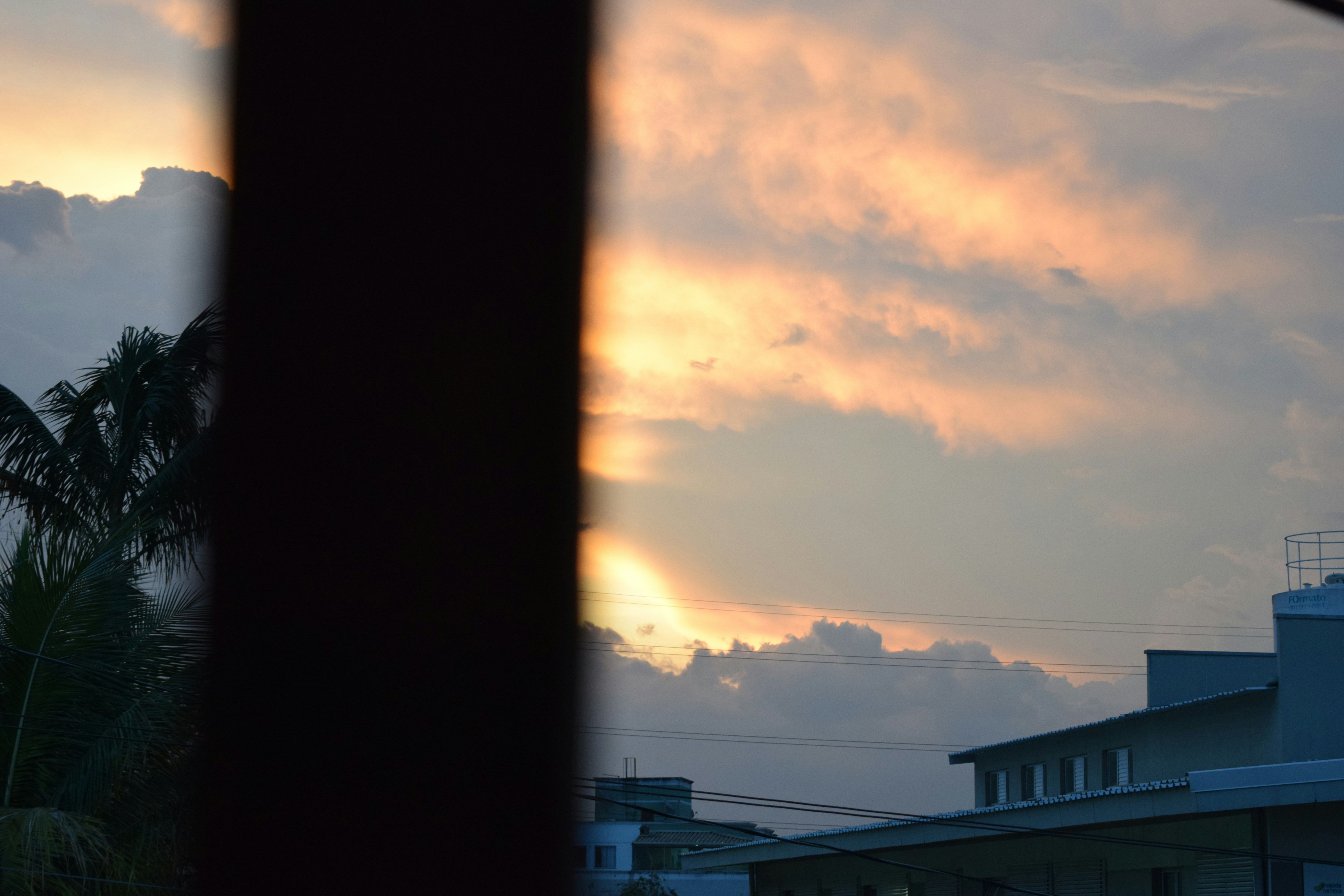 Sunset view through a window with silhouetted buildings and palm tree against colorful sky.