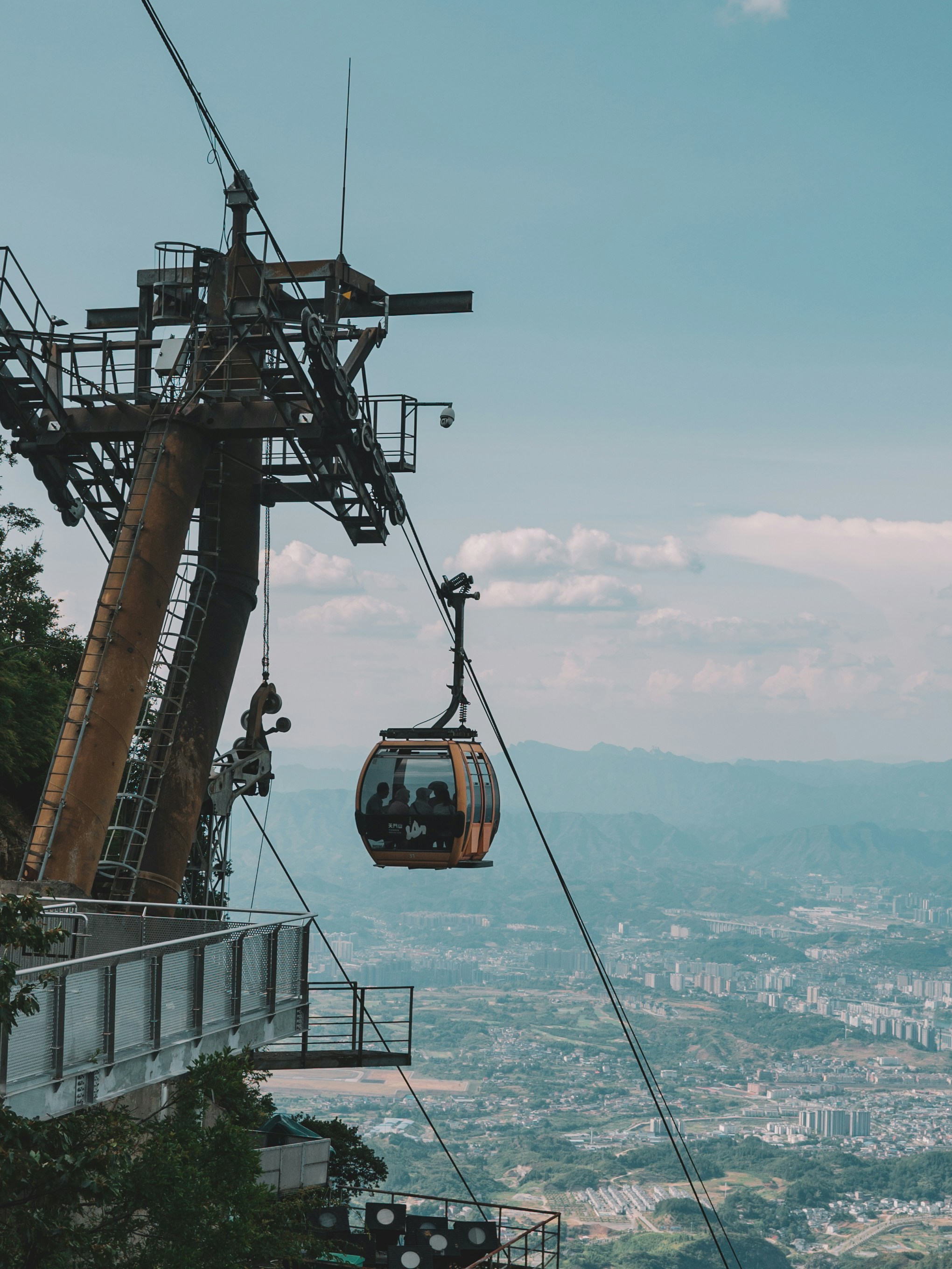 A cable car gliding smoothly along its track, suspended high above a sprawling urban landscape. The scene captures the blend of nature and modern engineering.