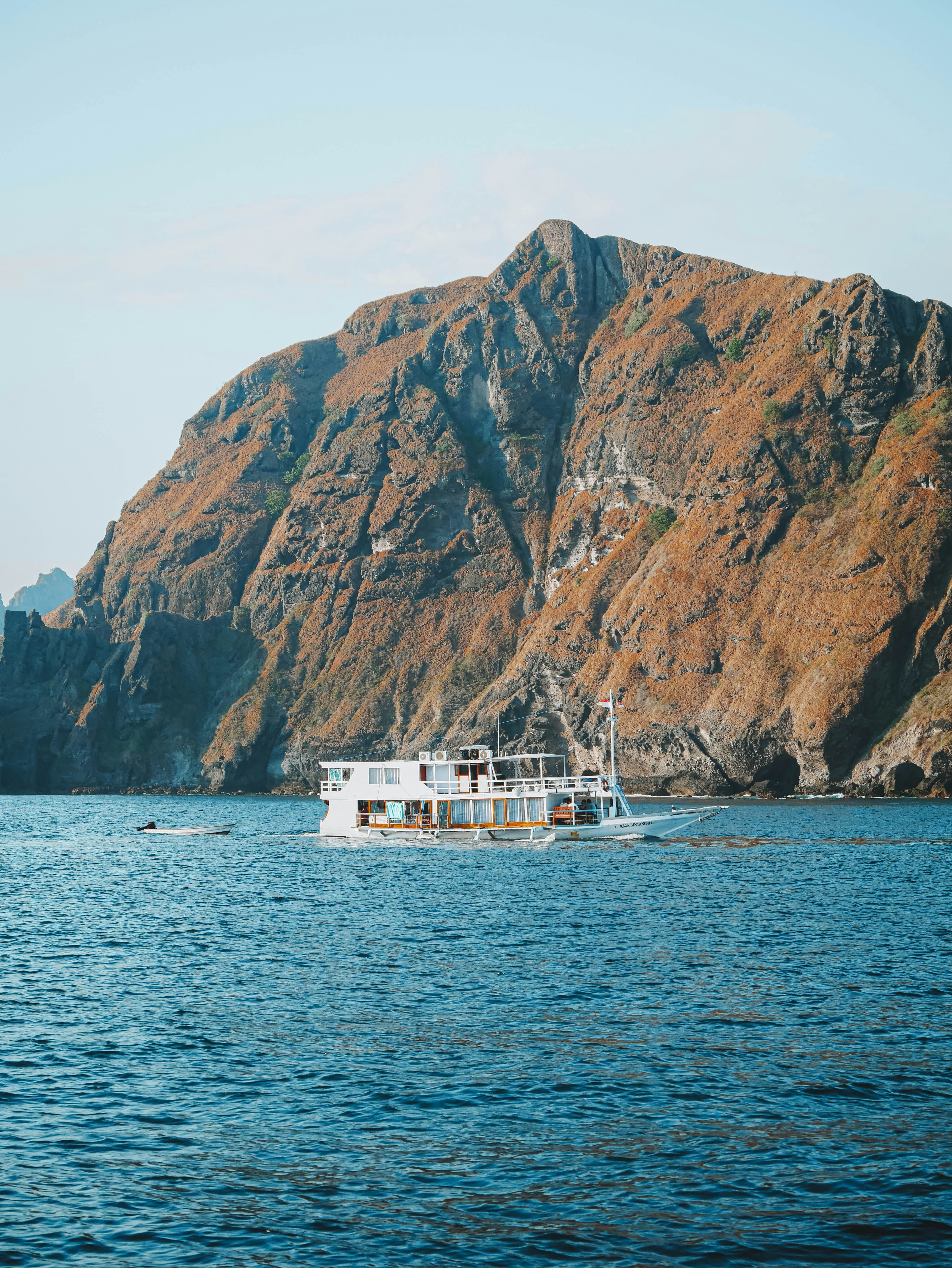 White Ferry Tracing a Lava-Orange Cliff over Quiet Blue Waters