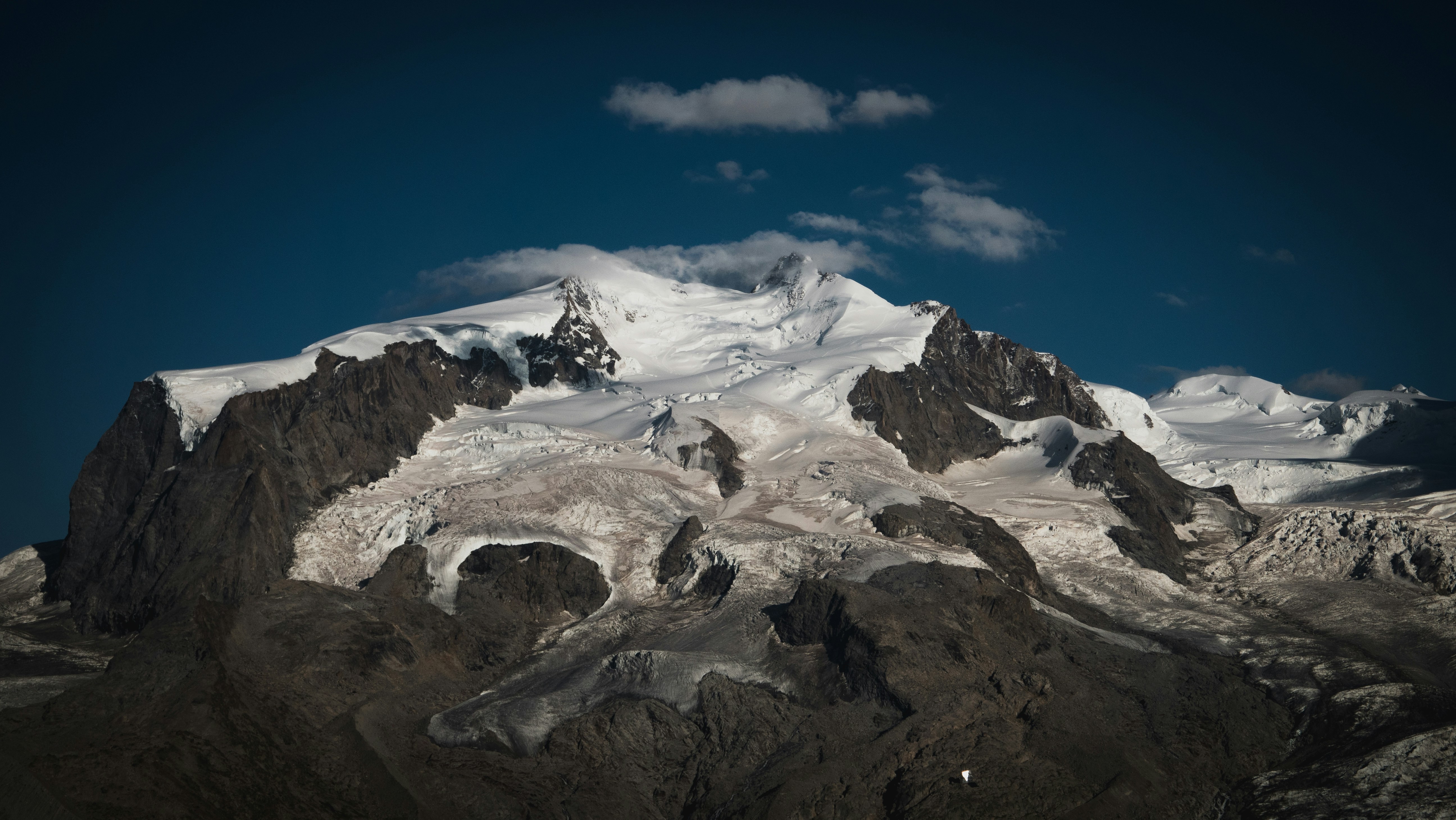 Snow-Crowned Summit Rising Over a Rugged Ridge Under a Clear Blue Sky