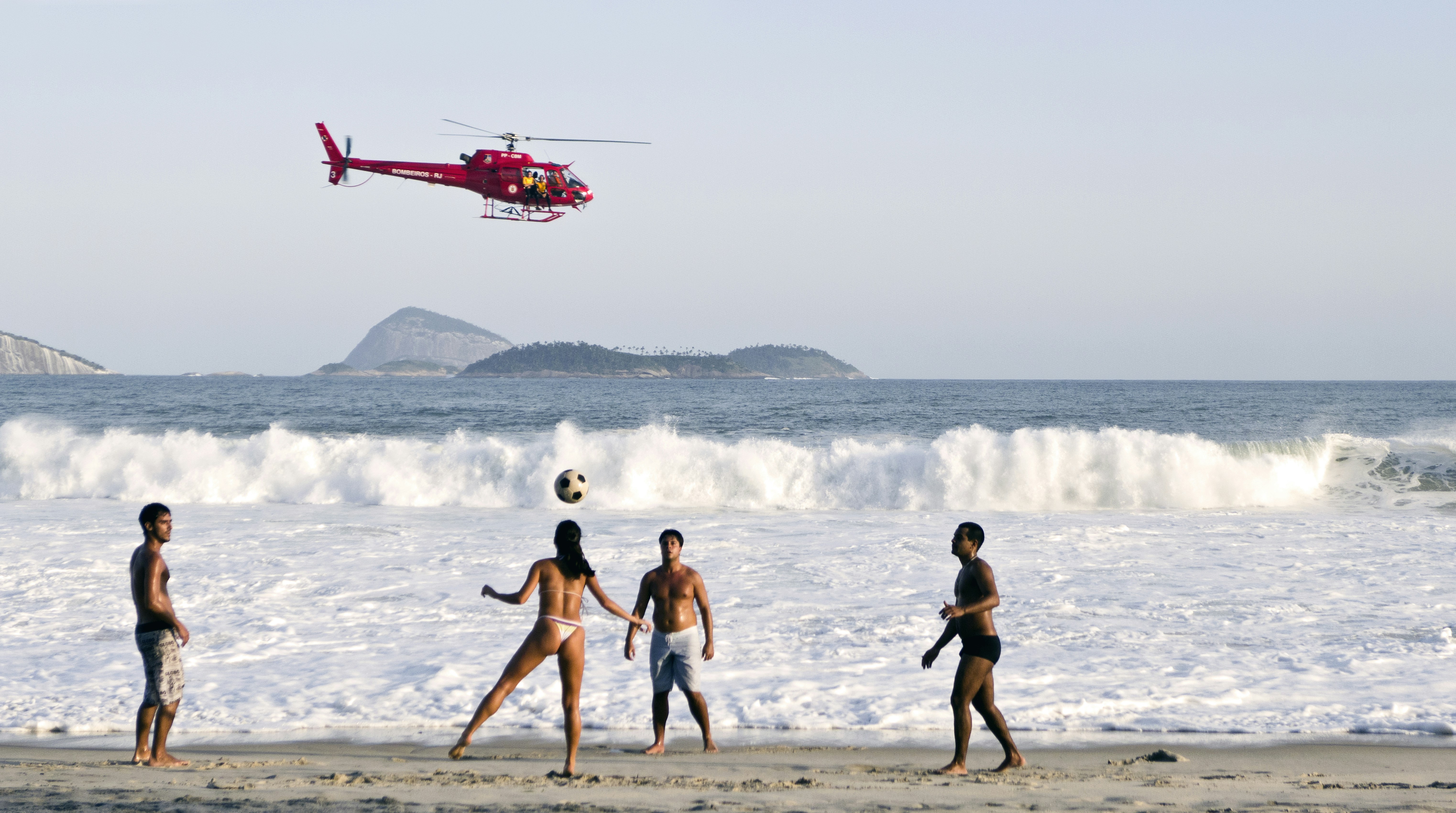 Crimson Helix over the Beach: Helicopter Pause Above Surf and Sun