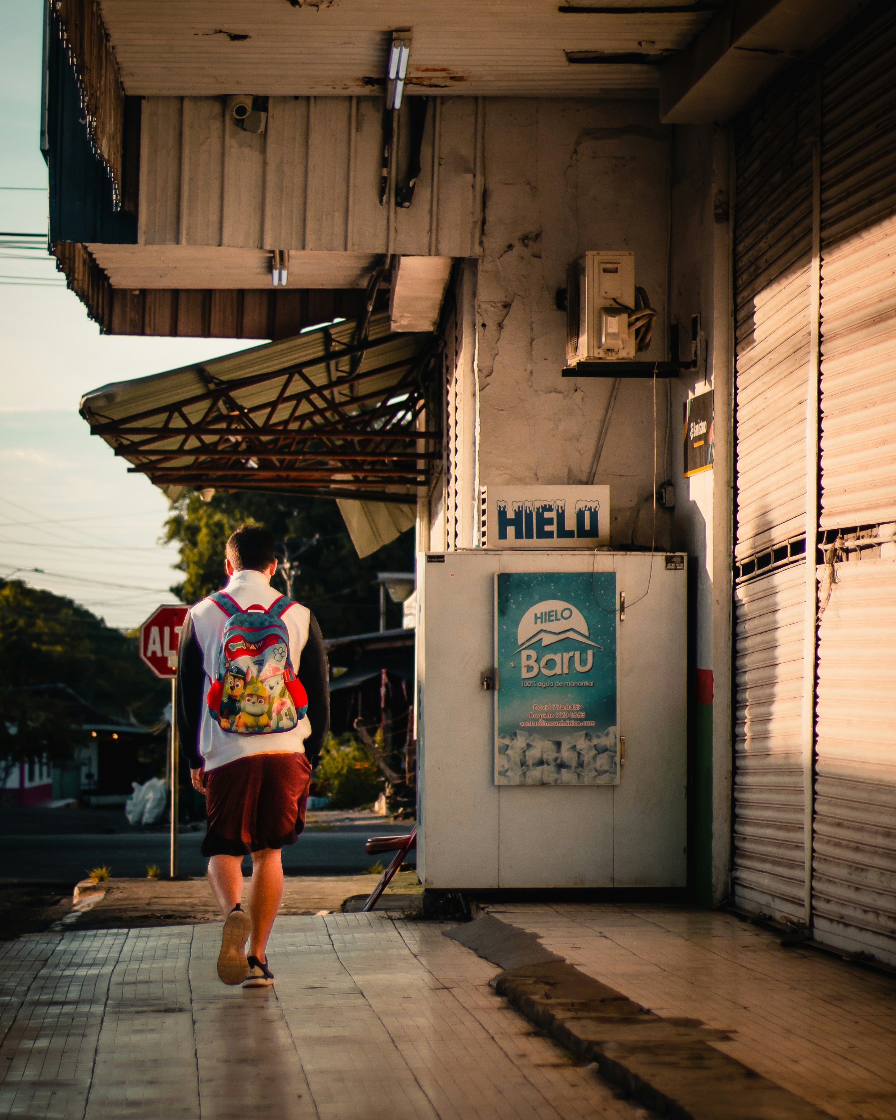 Sunlit Backstreet Stroll: A Backpacker Moves Past a Quiet Shopfront