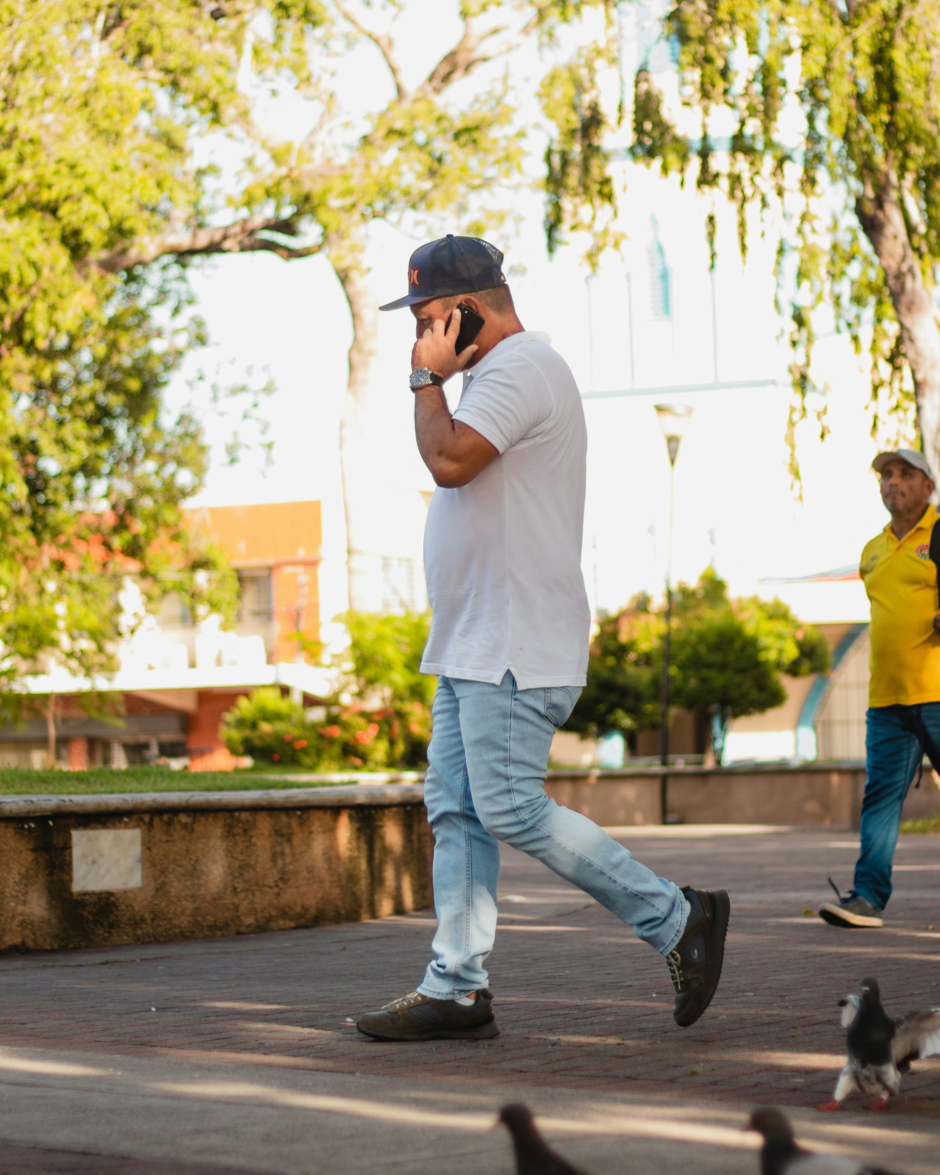 Sunlit Stroll: A Man on a Phone Through a City Plaza