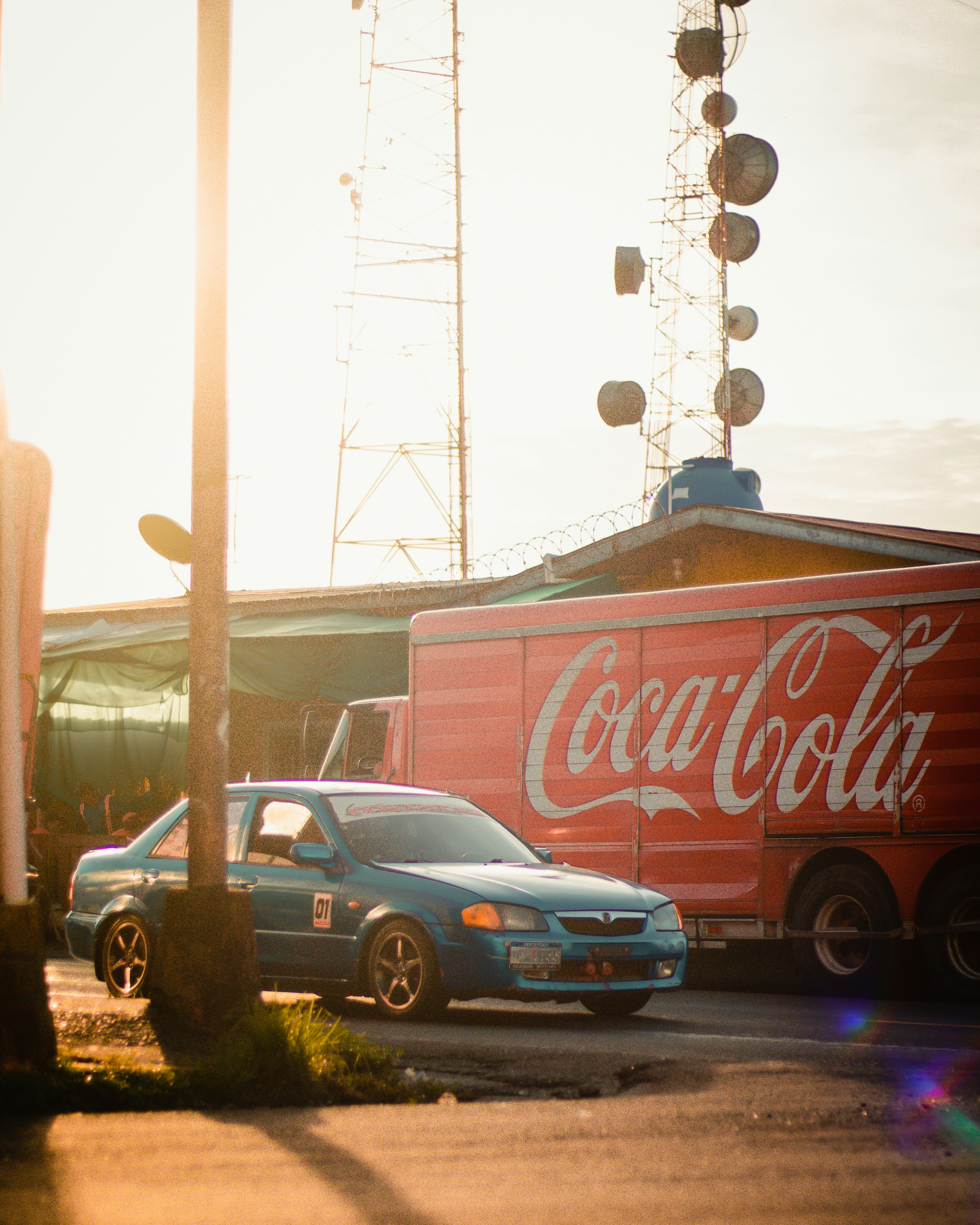 Sunset Glow Over a Coca-Cola Truck and a Blue Sedan