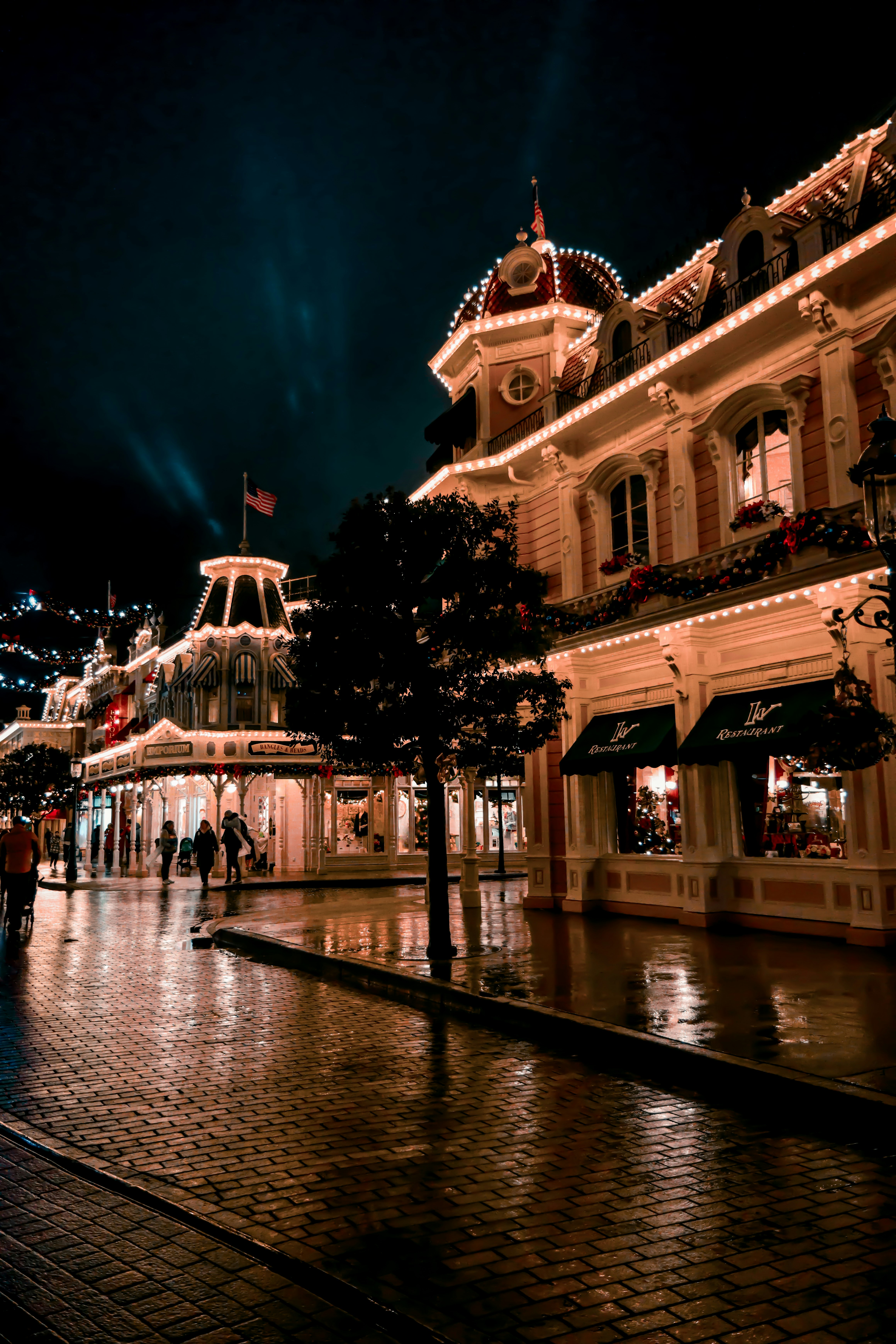 Illuminated storefronts and reflections on wet pavement create a magical atmosphere in a bustling evening scene.
