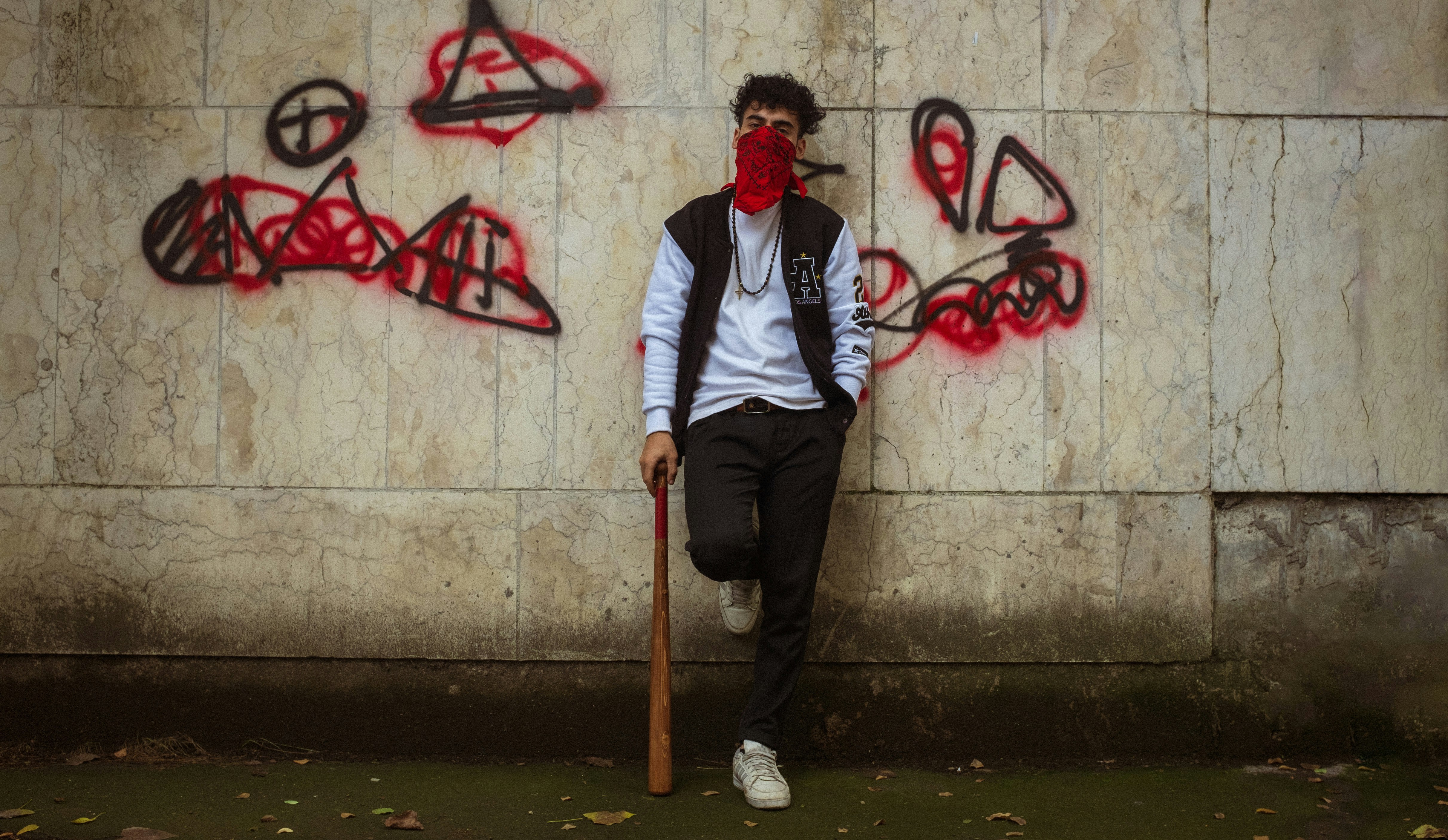 A man with a baseball bat leaning against a wall covered in graffiti ...