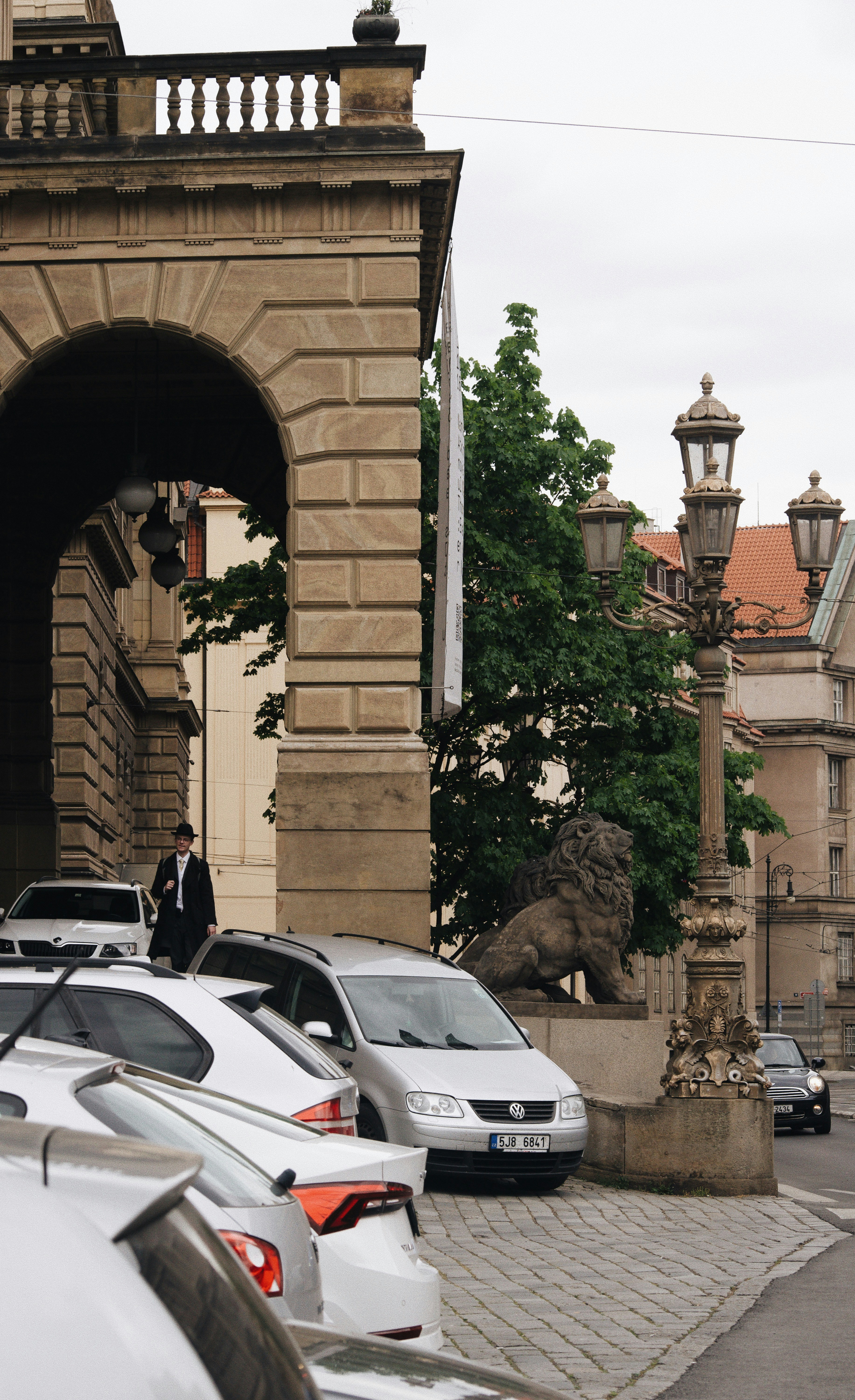 Stone Arch, Row of Cars, and a Watchful Lion Under Ornate Lamps