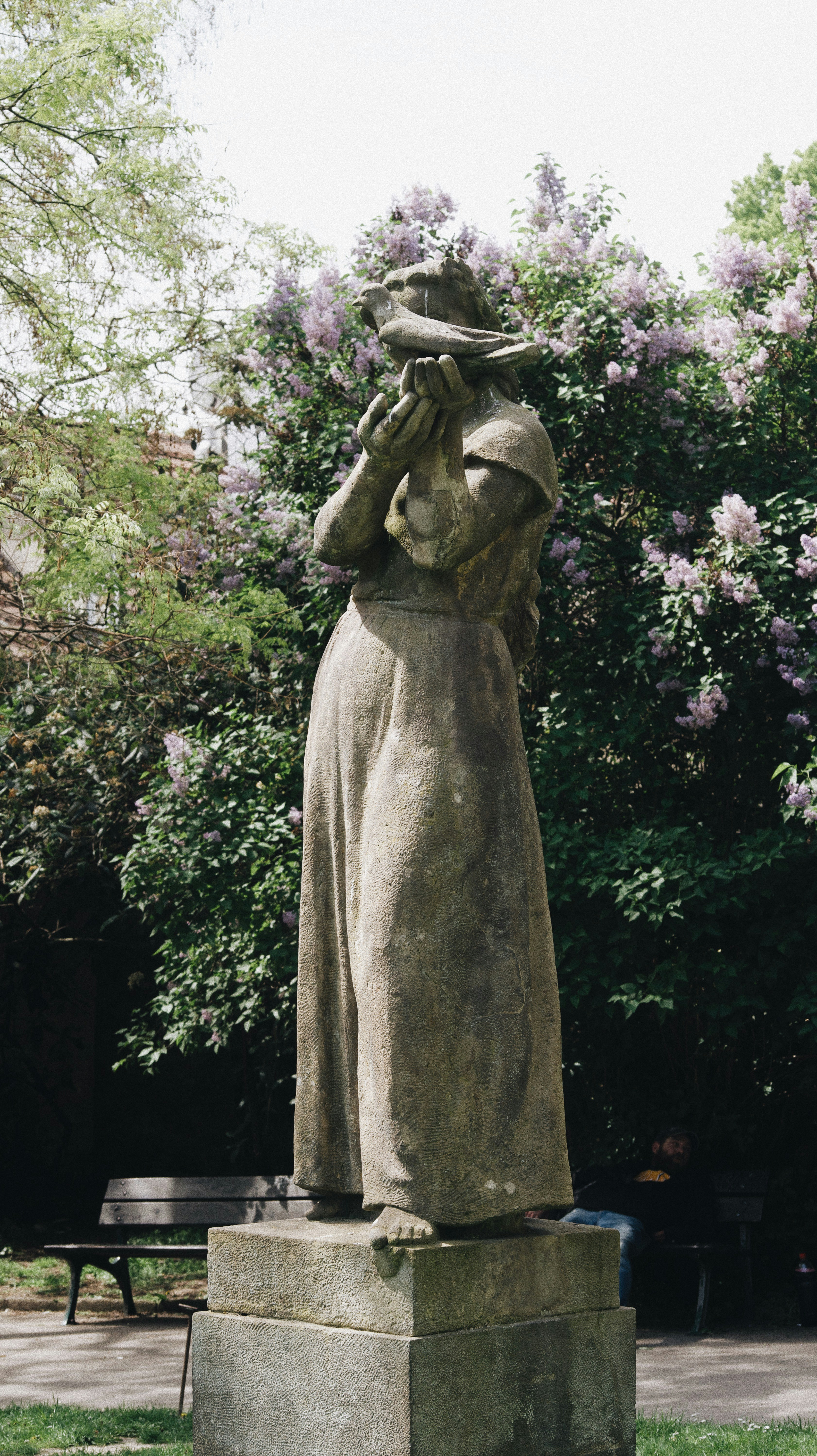 Stone Guardian Cradling a Bird Amid Lilac Bouquets