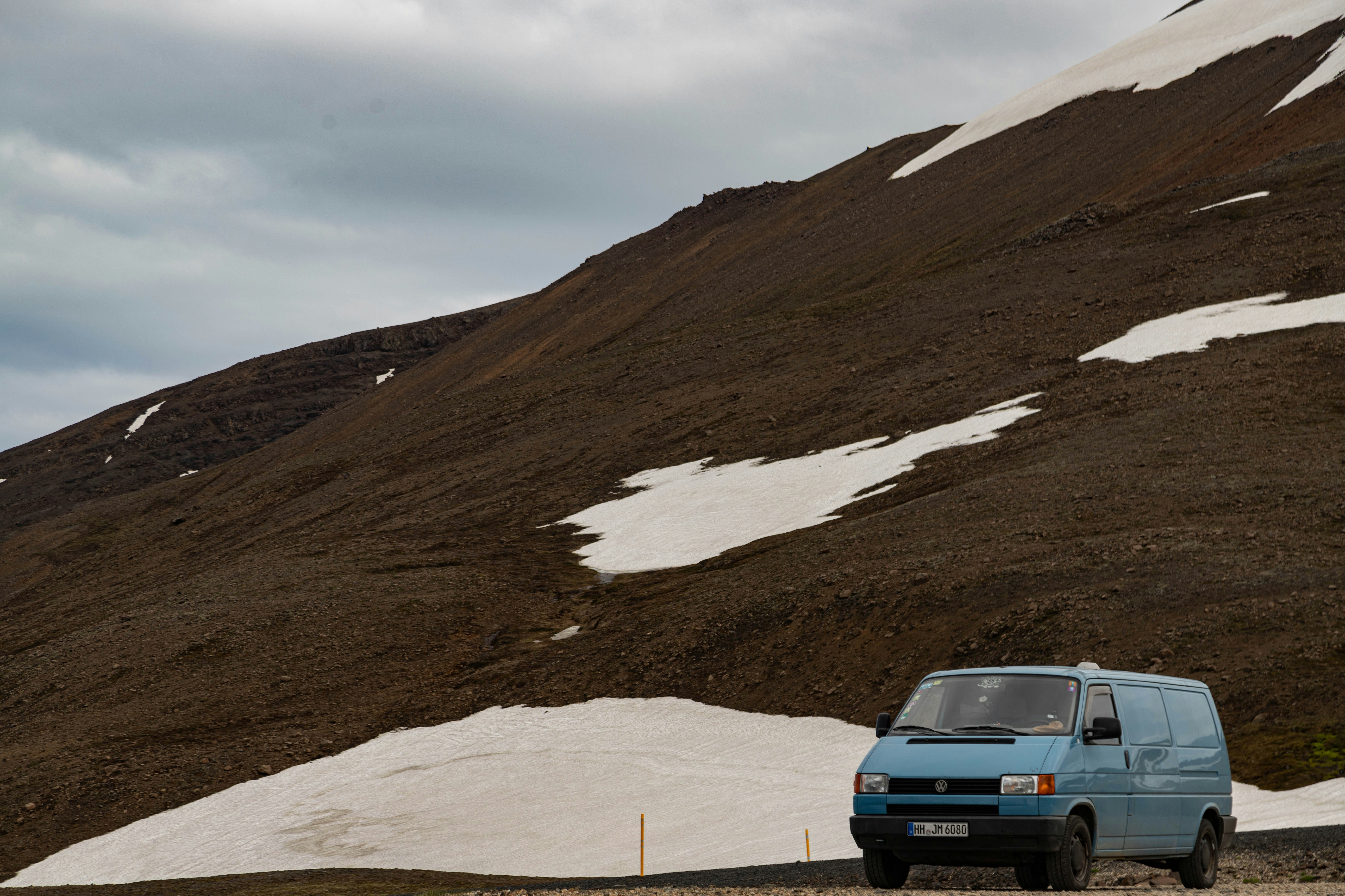 Blue Van on a Snow-Dusted Slope Under Moody Skies