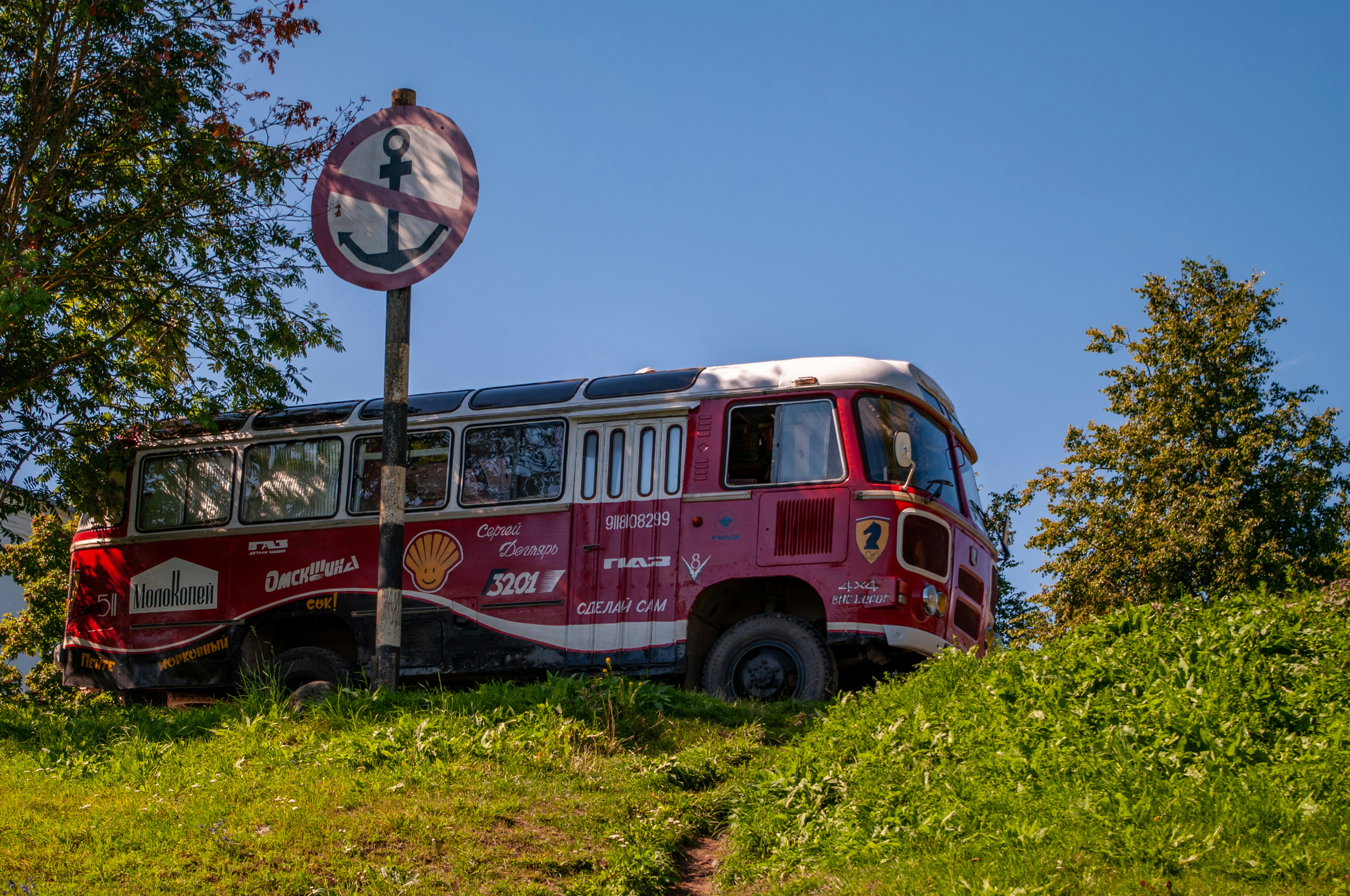 Red vintage bus parked on a grassy hill beside a no-anchor sign under a clear blue sky.