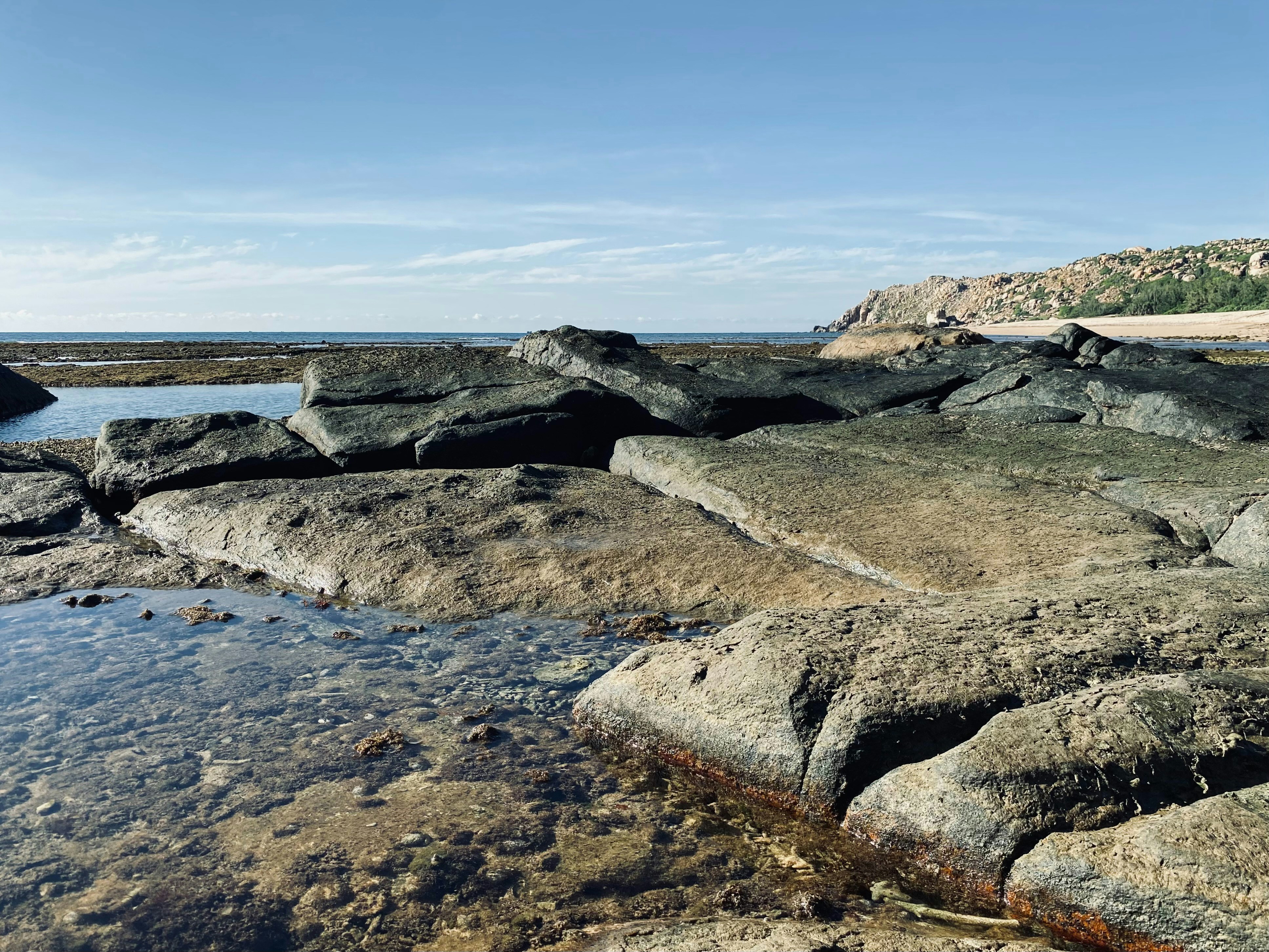 Rugged rocks and shallow pools under a clear blue sky.