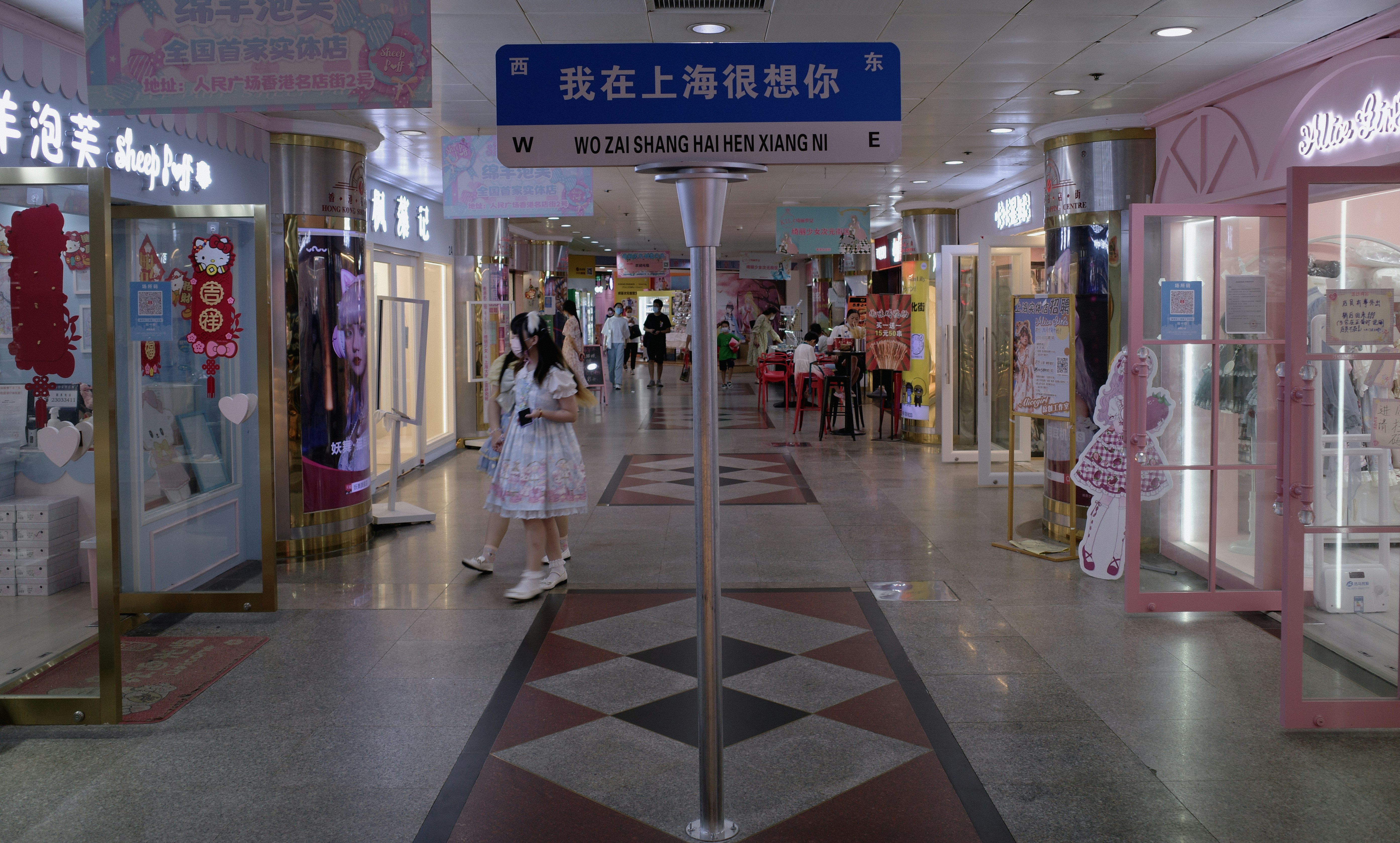 Central Shanghai shopping arcade with a blue overhead sign, pink storefronts, and shoppers on a checkered tile floor.