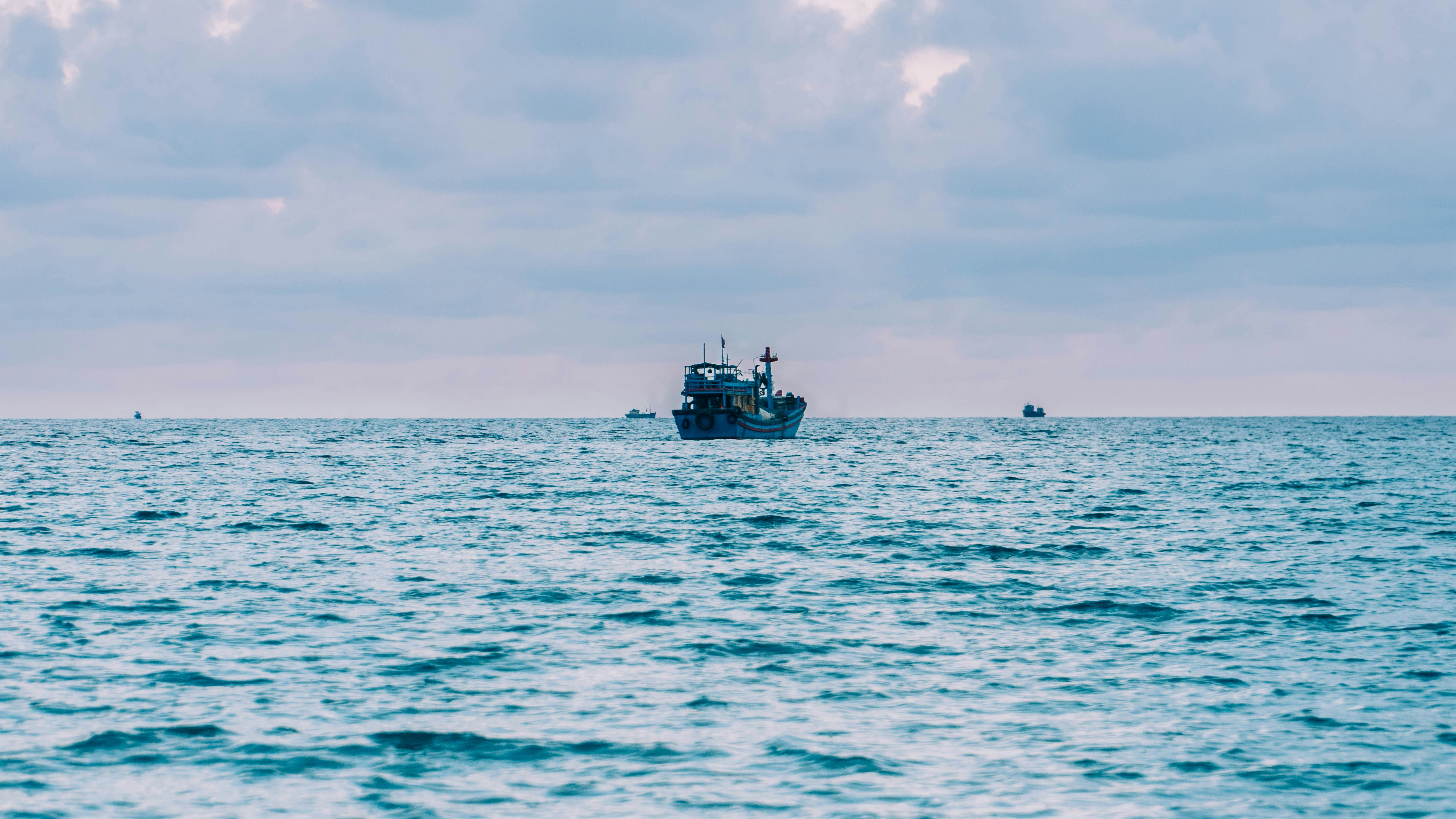 Fishing boat navigating the expansive ocean under a cloud-laden sky.
