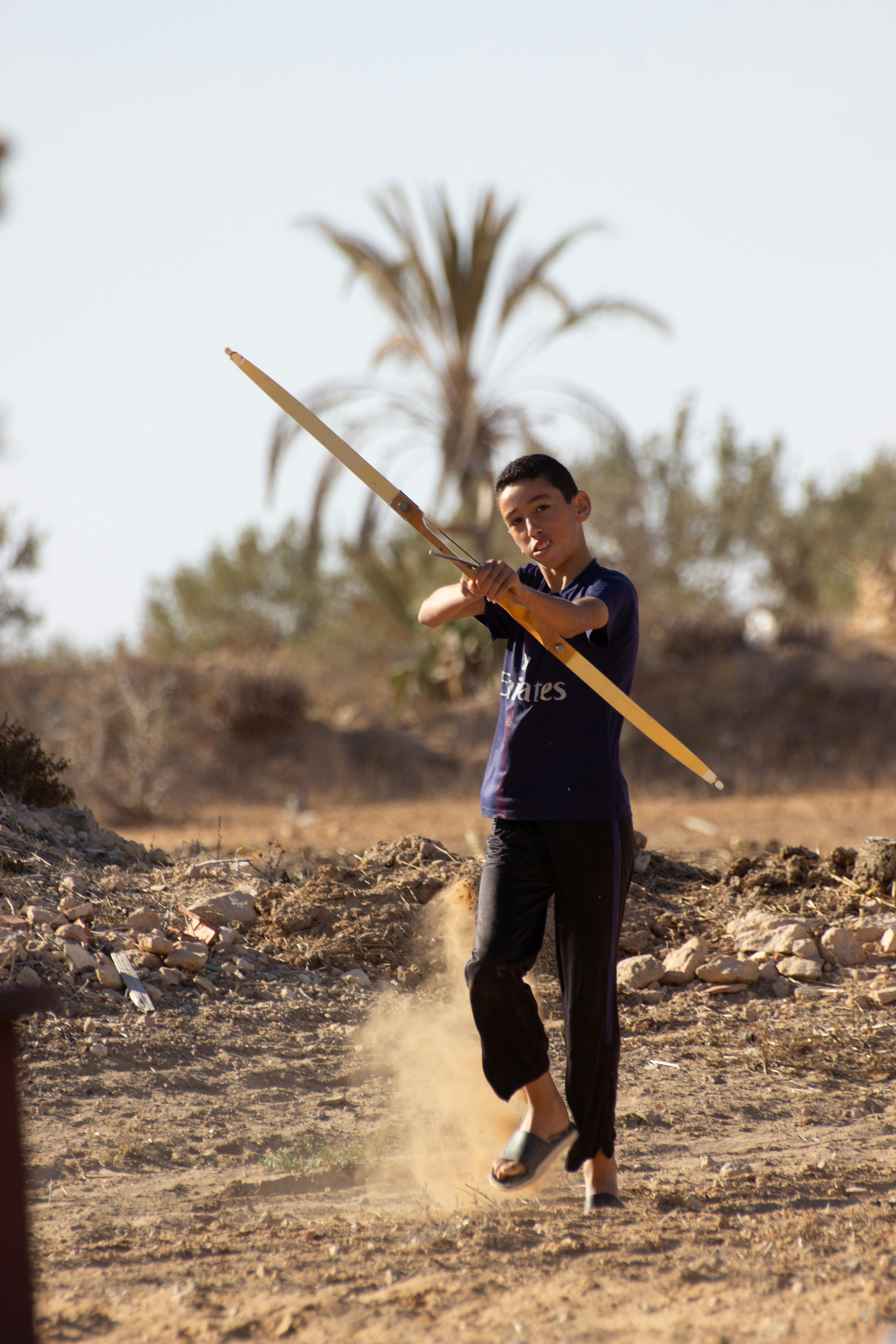 Desert Spearplay: A boy wields a long wooden staff mid-stride in sunlit dust