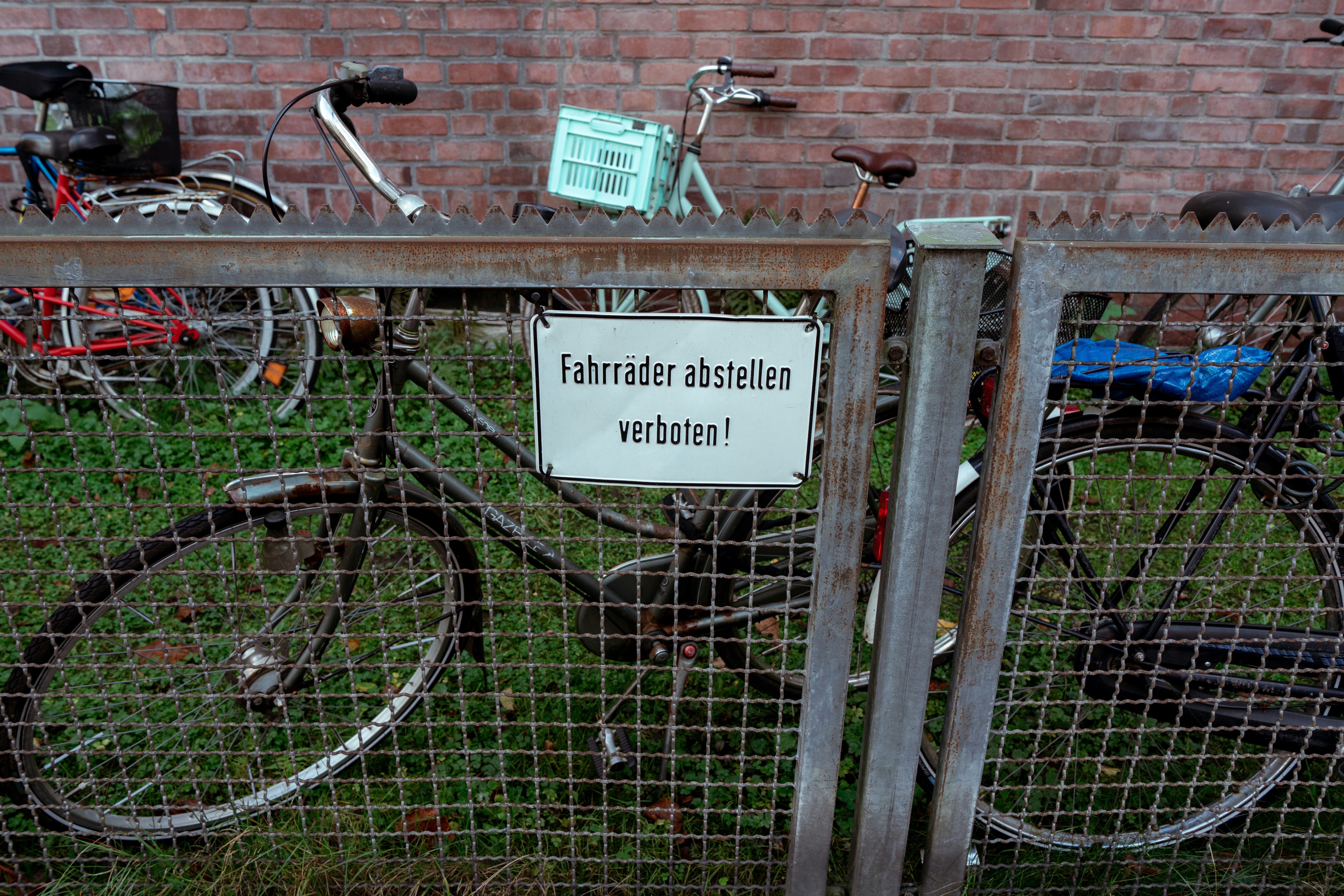 Bicycles parked behind a wire fence with a sign prohibiting bicycle parking.