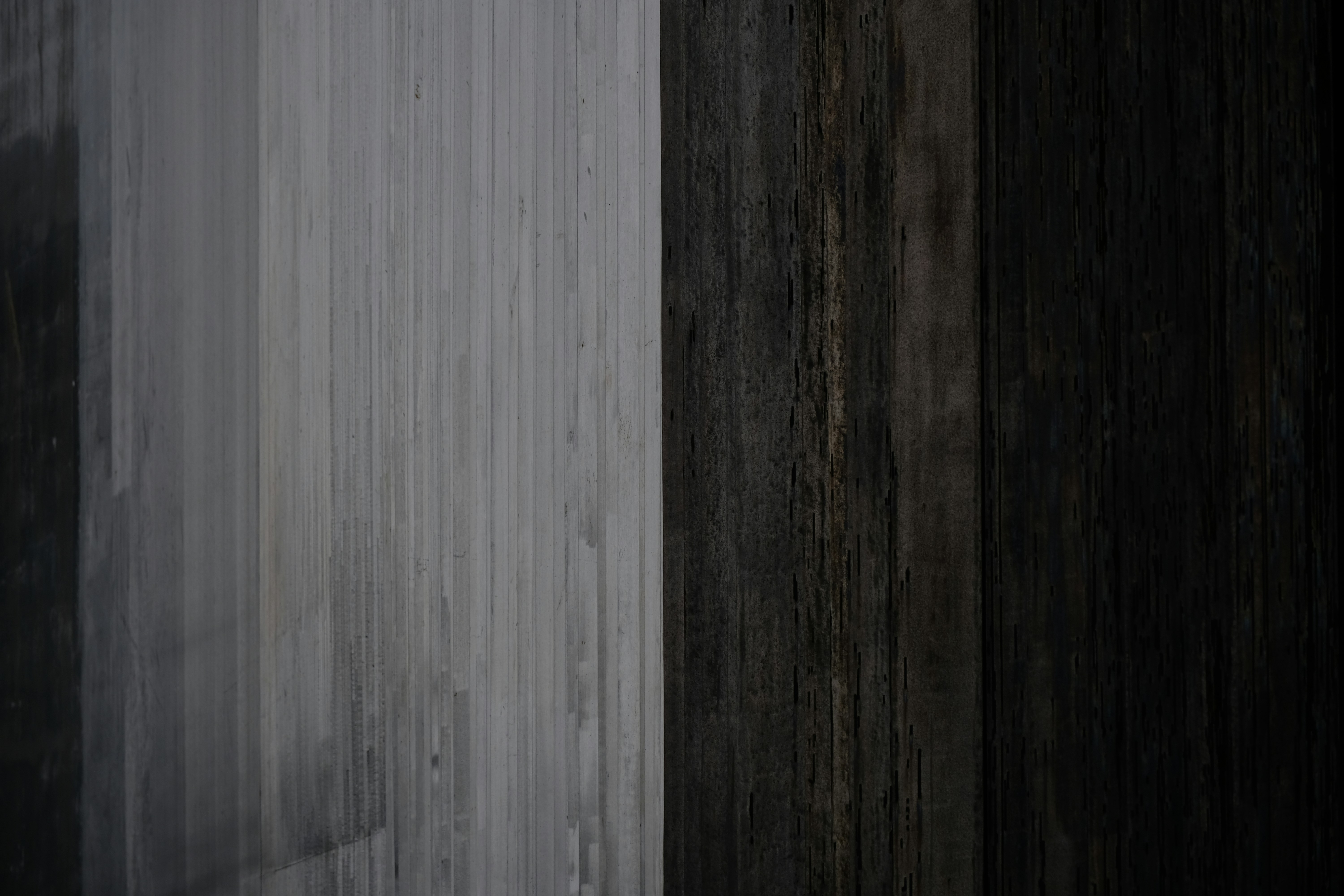 This image captures the striking contrast between two juxtaposed surfaces, one light and one dark. The vertical lines create a rhythmic texture, enhancing the visual intrigue. The subtle play of light and shadow adds depth to the monochromatic palette, creating a moody and contemplative atmosphere.