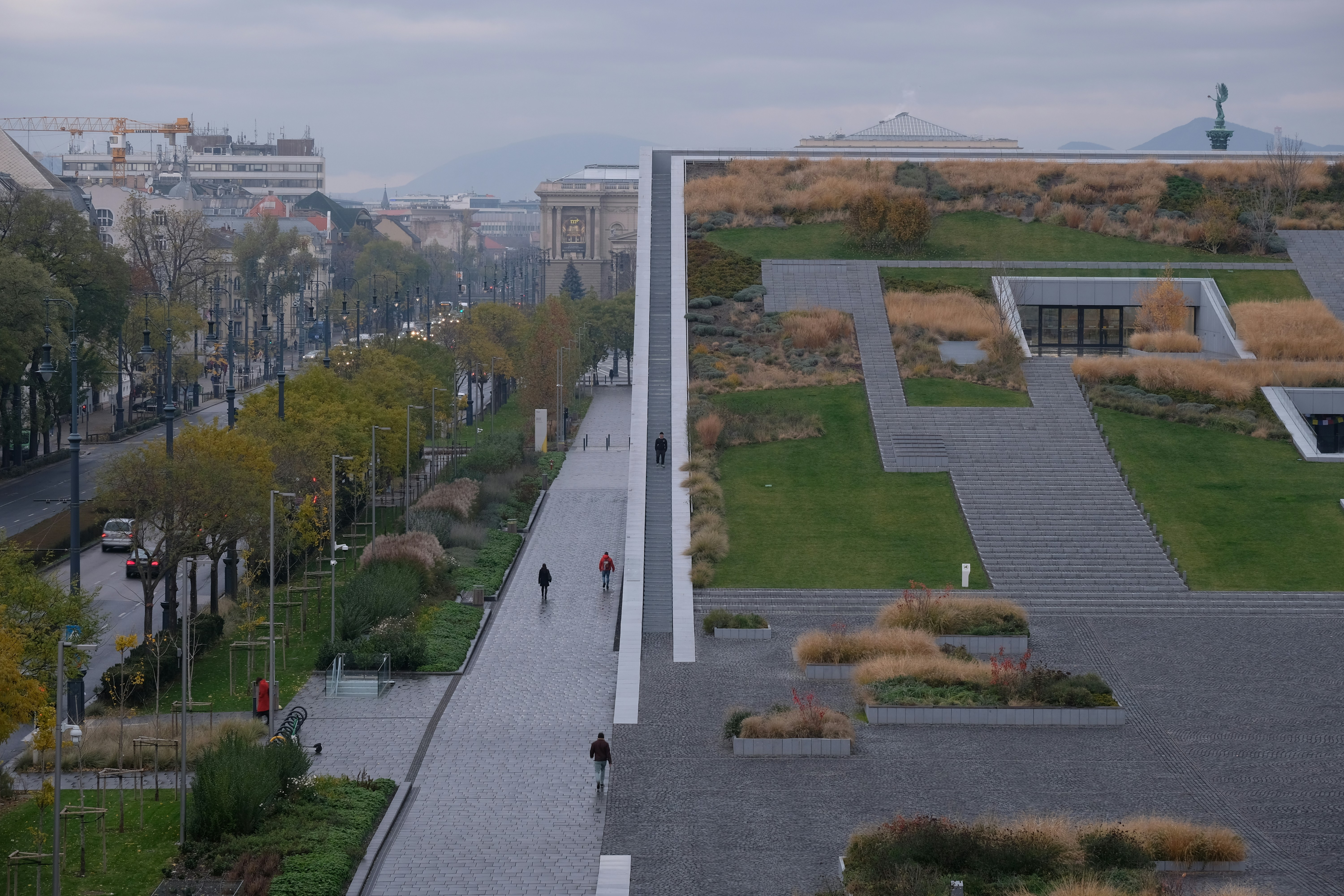 Modern architectural landscape featuring a green rooftop and urban pathways, with people leisurely walking in a city setting.
