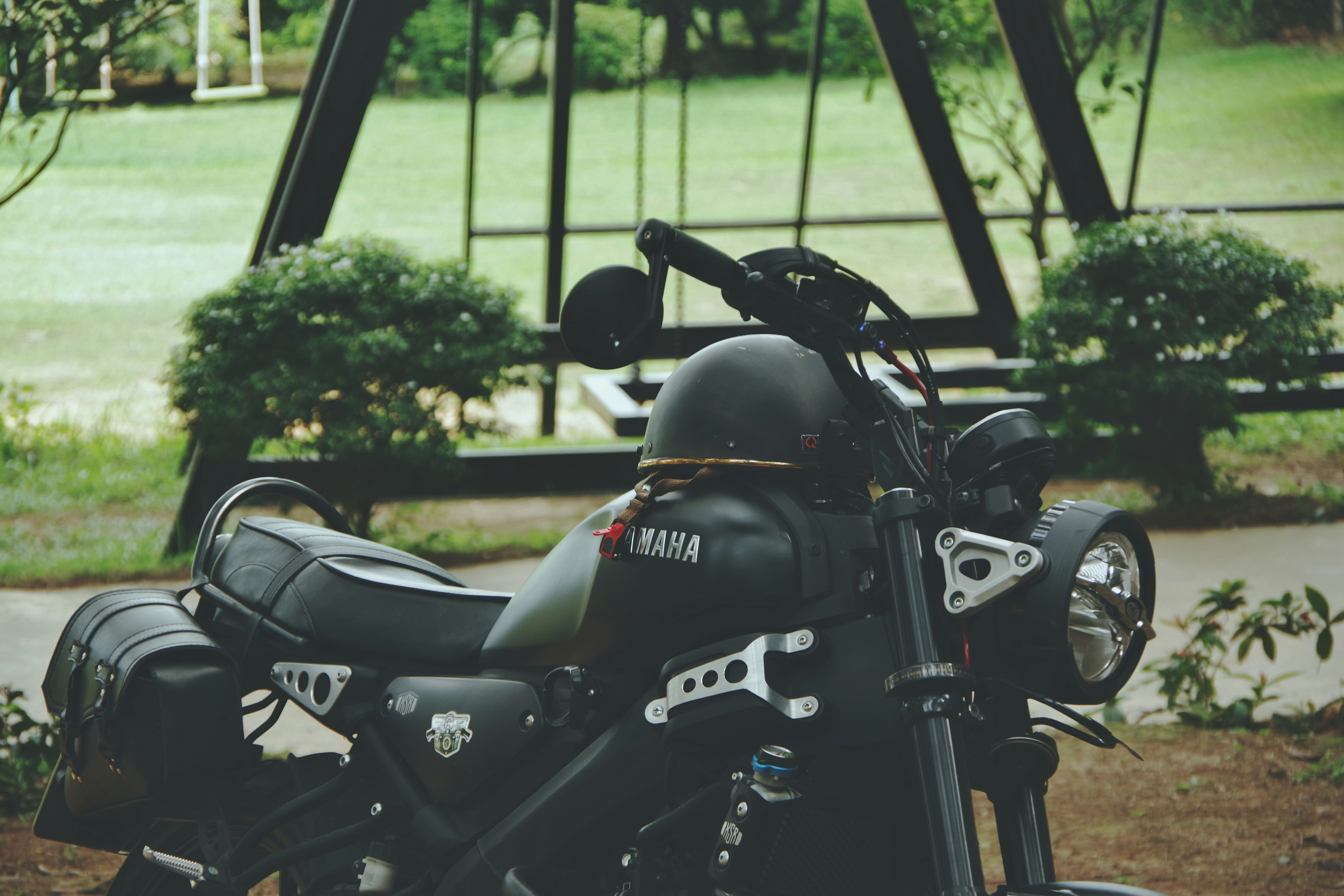 Yamaha motorcycle parked near a swing set, surrounded by lush greenery and soft grass.