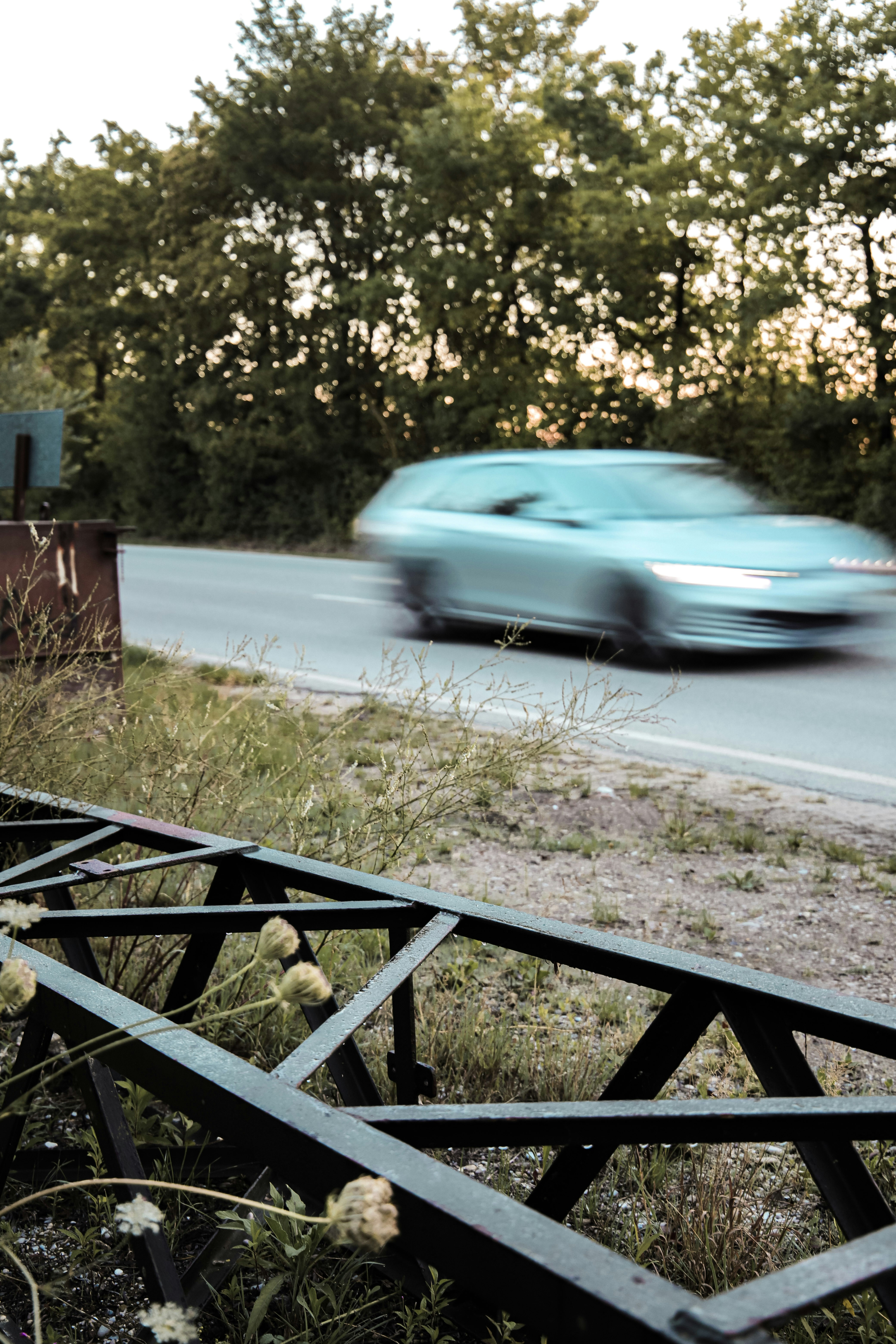 Blurred blue hatchback in motion above a grassy verge with rusted metal framework foreground