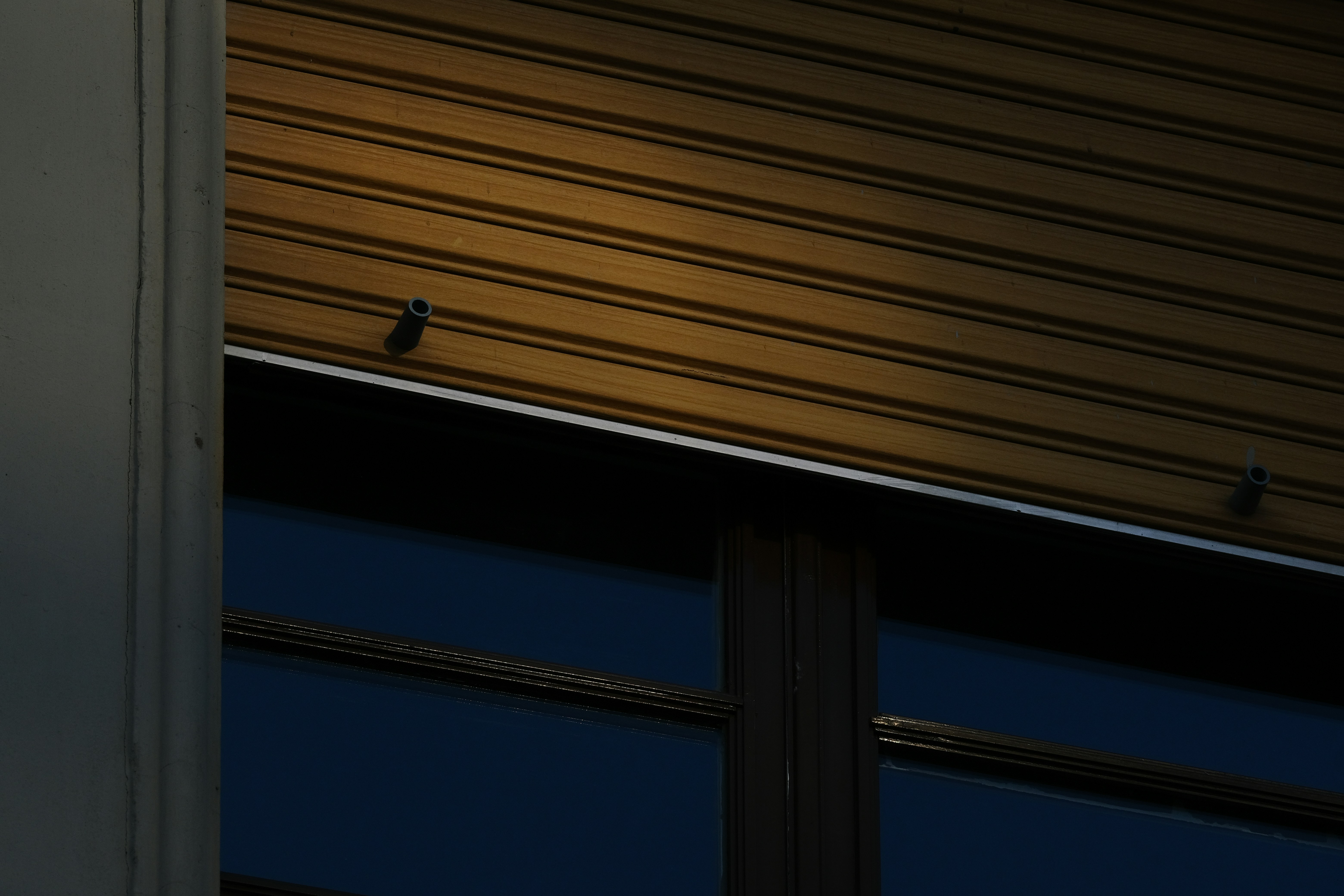 Blue Window Beneath a Warm Wooden Shutter at Dusk