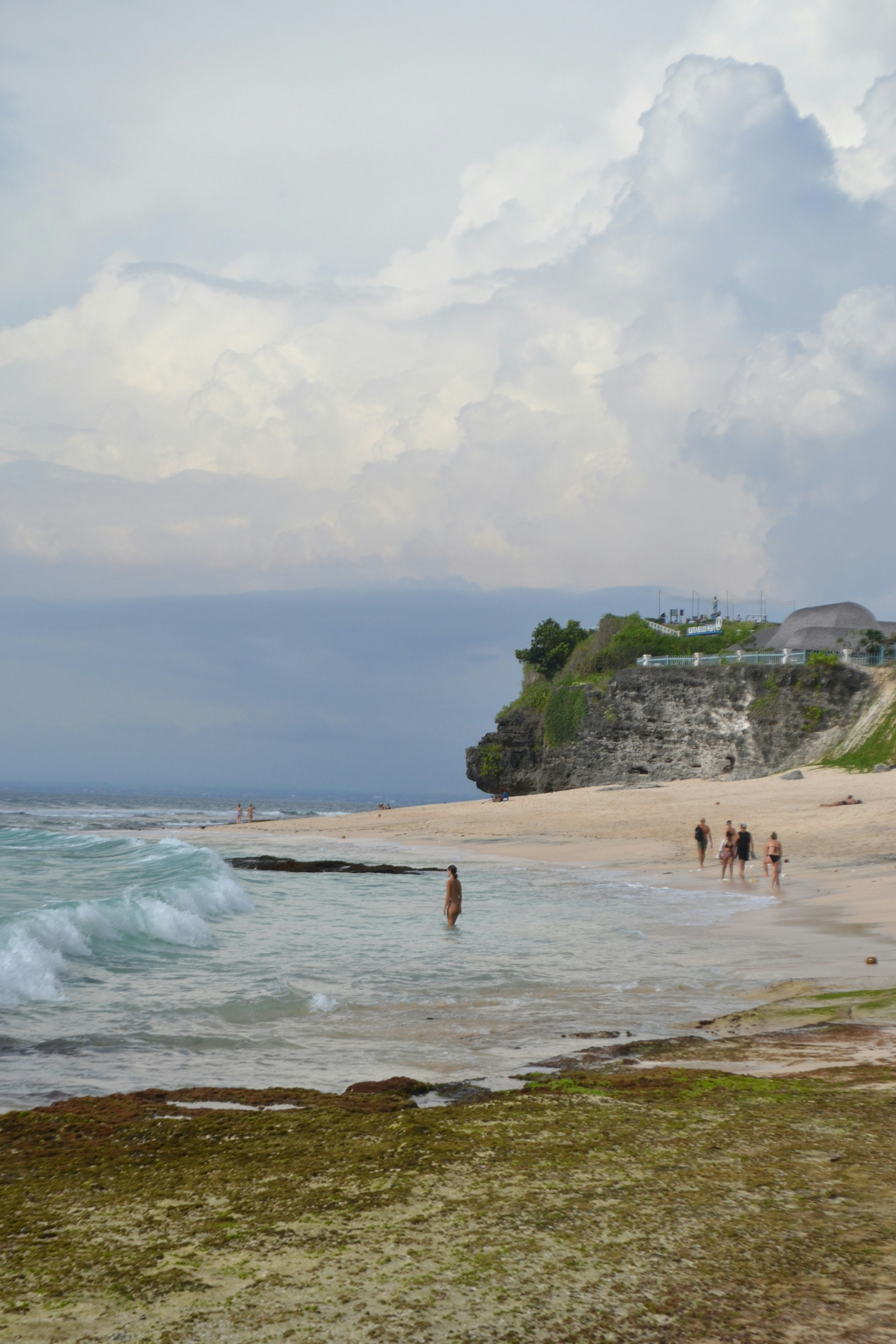 Clifftop Beachfront: Walkers on a Sunlit Shore Beneath Ocean Mists