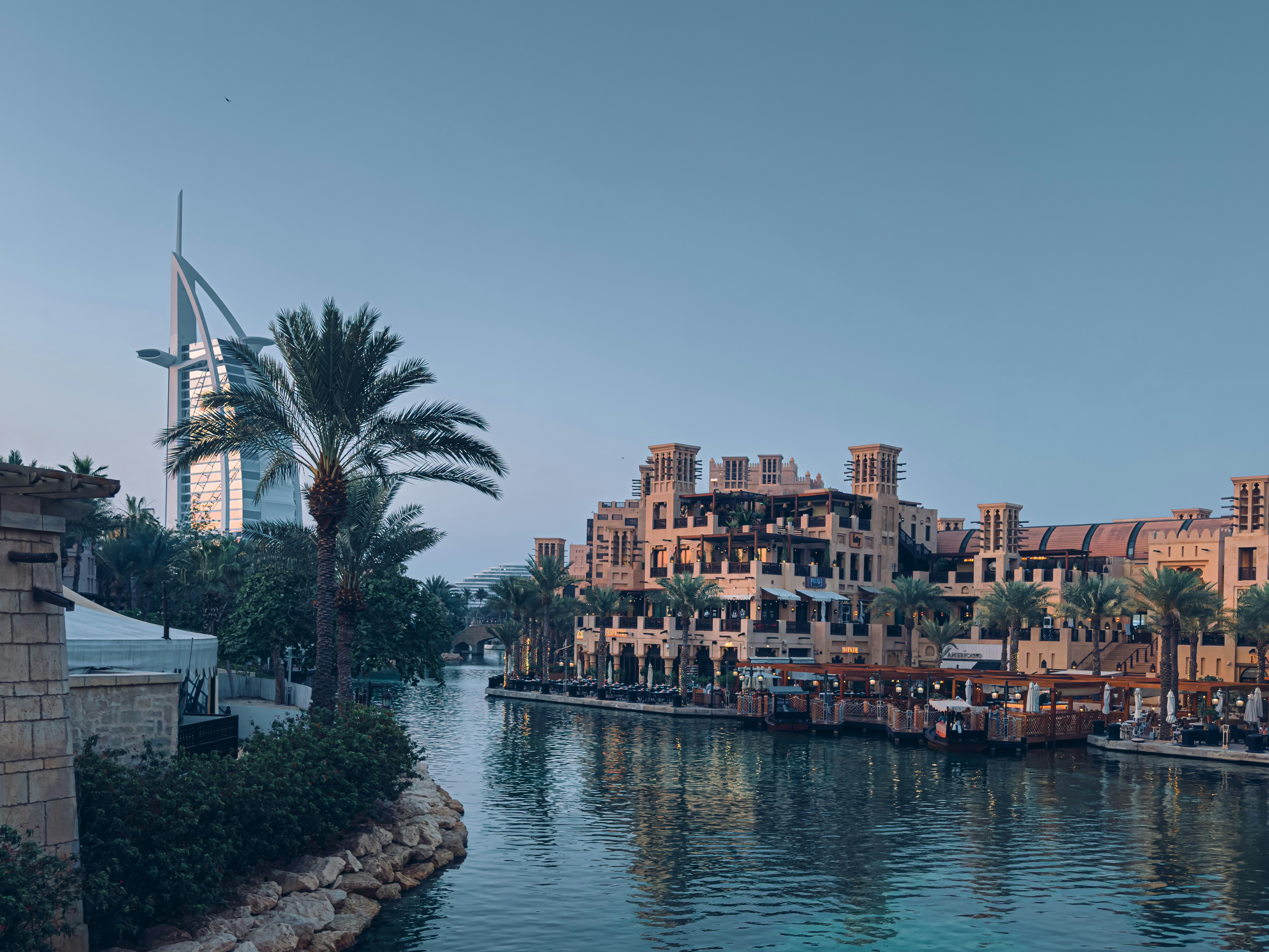 Palm trees and traditional architecture frame the Burj Al Arab against a serene waterway.