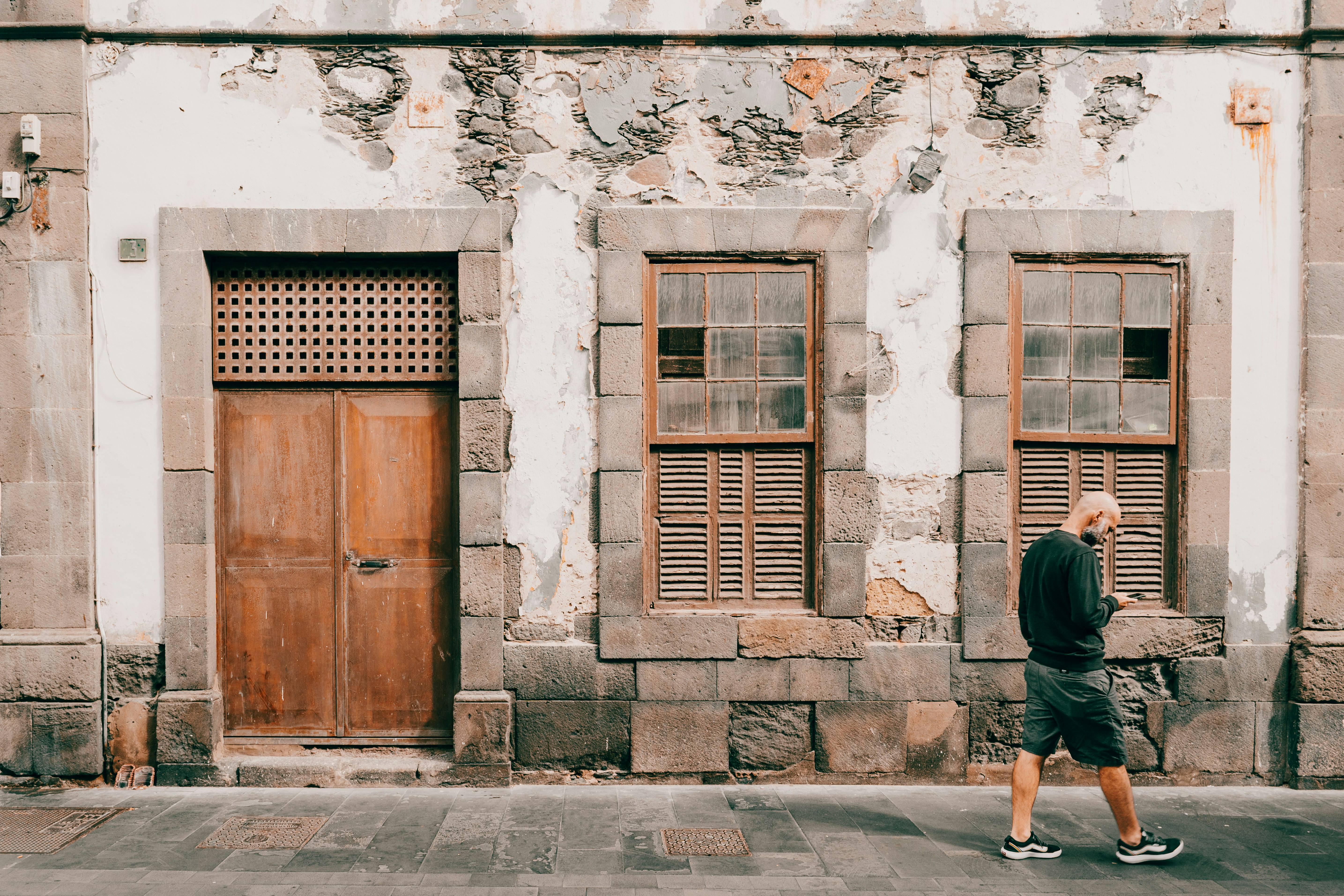 Person walks past a weathered building with peeling paint and wooden doors in Vegueta, Las Palmas.