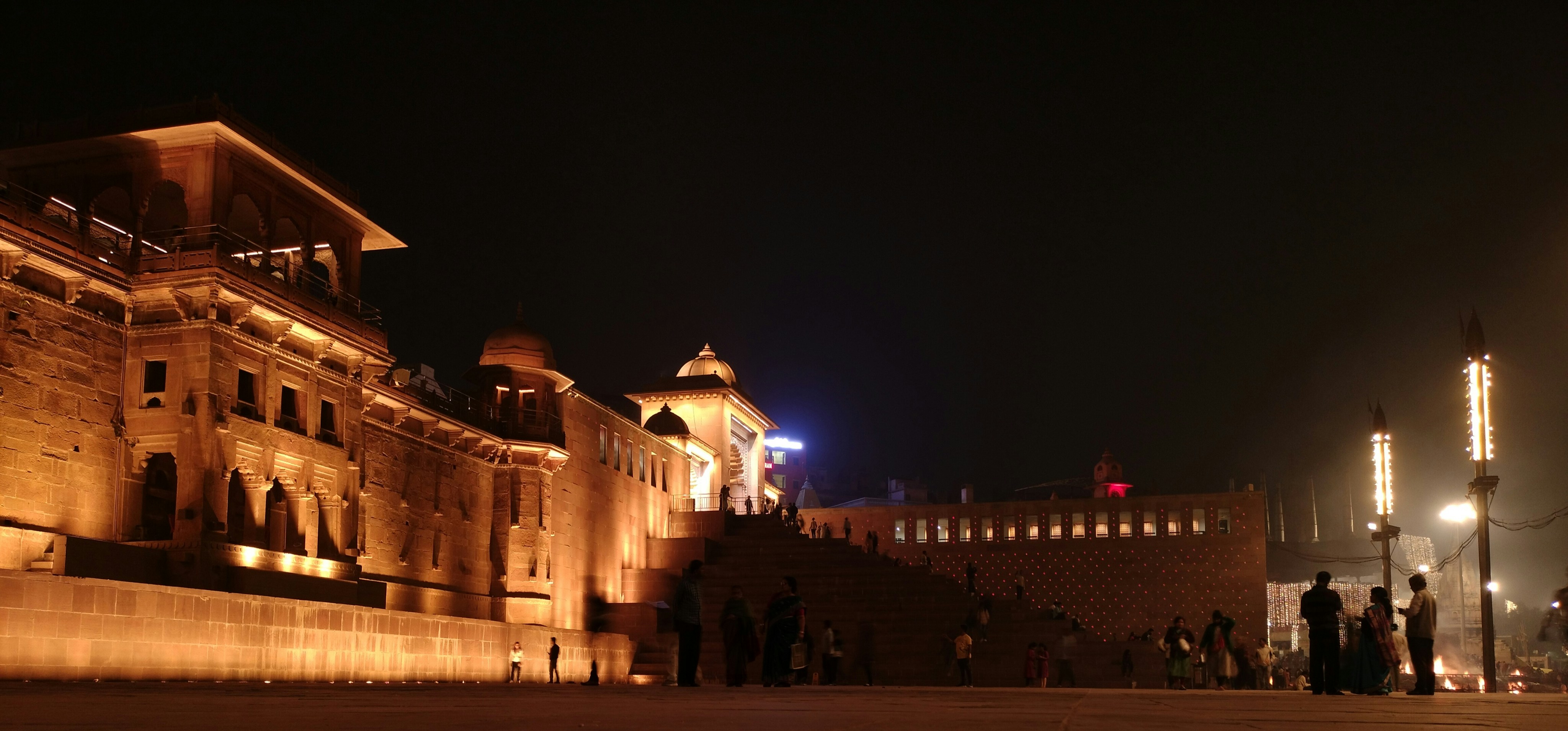 Night view of Kashi Vishwanath Corridor with illuminated architecture and silhouettes of people.